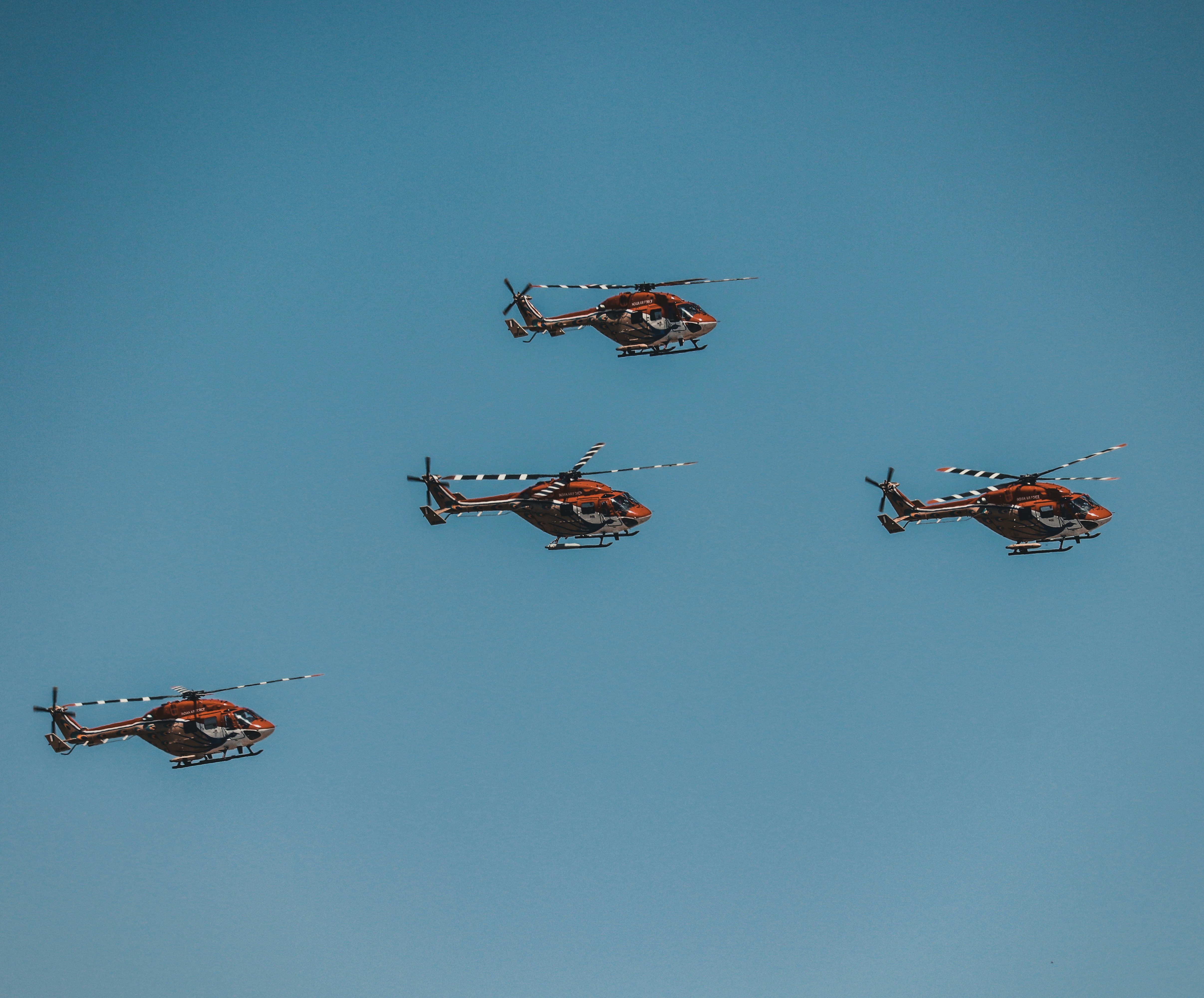 Four helicopters in synchronized flight against a clear blue sky, showcasing precision and coordination.