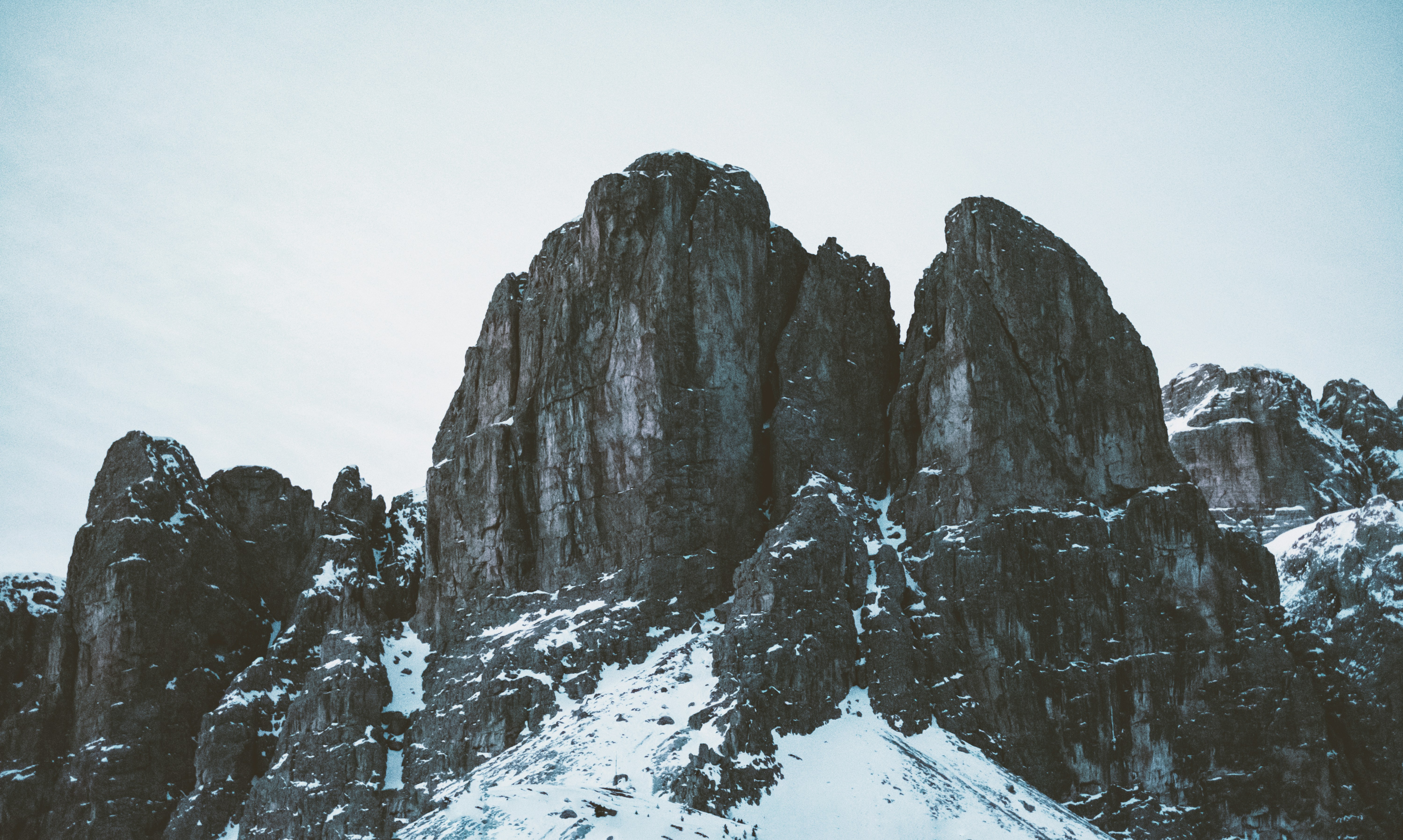 Snow-dusted Brunecker Turm peaks rise against a pale sky in the Dolomites.