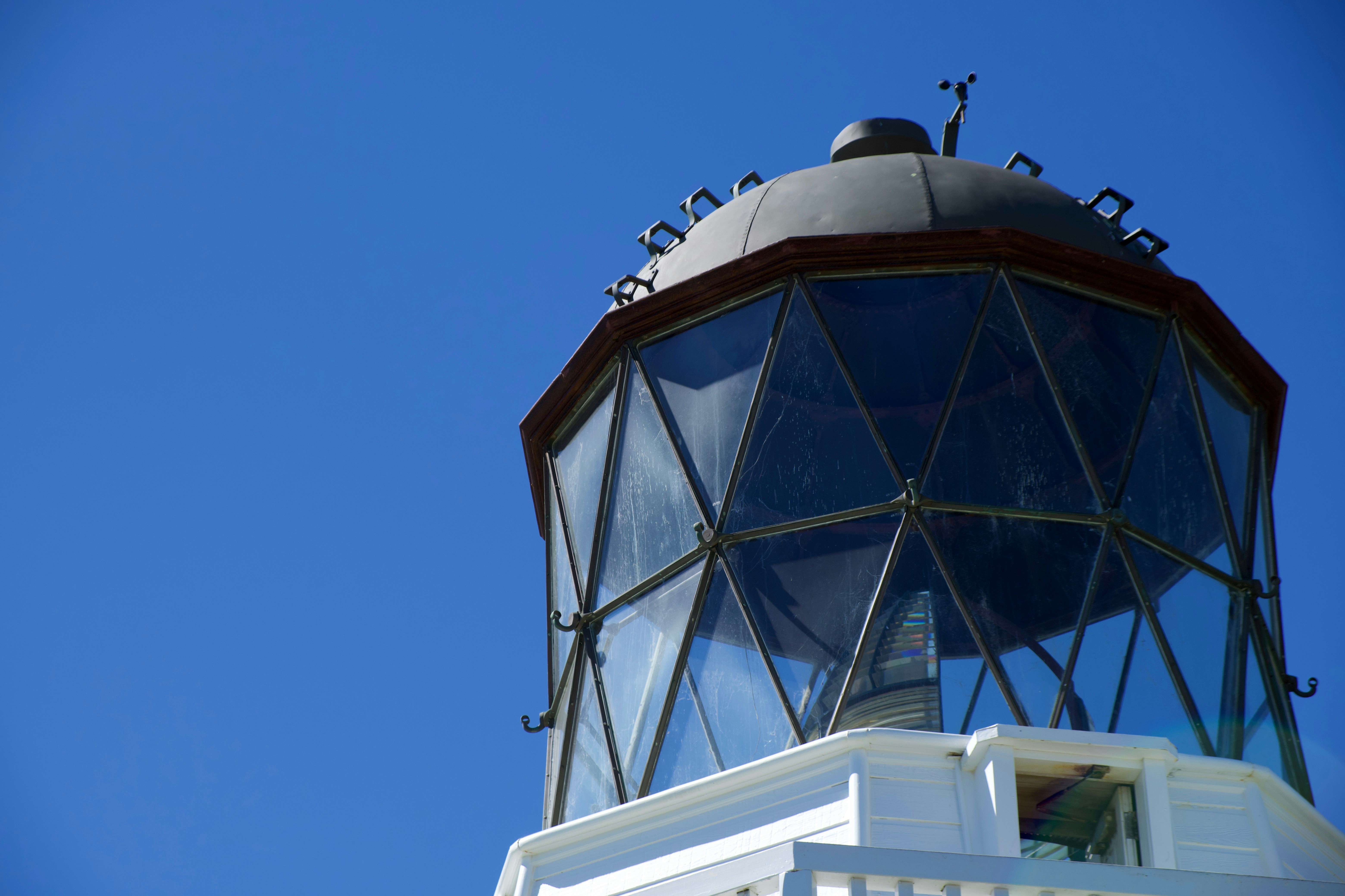 The glass lantern room of a lighthouse against a clear blue sky, showcasing its intricate design and functionality.
