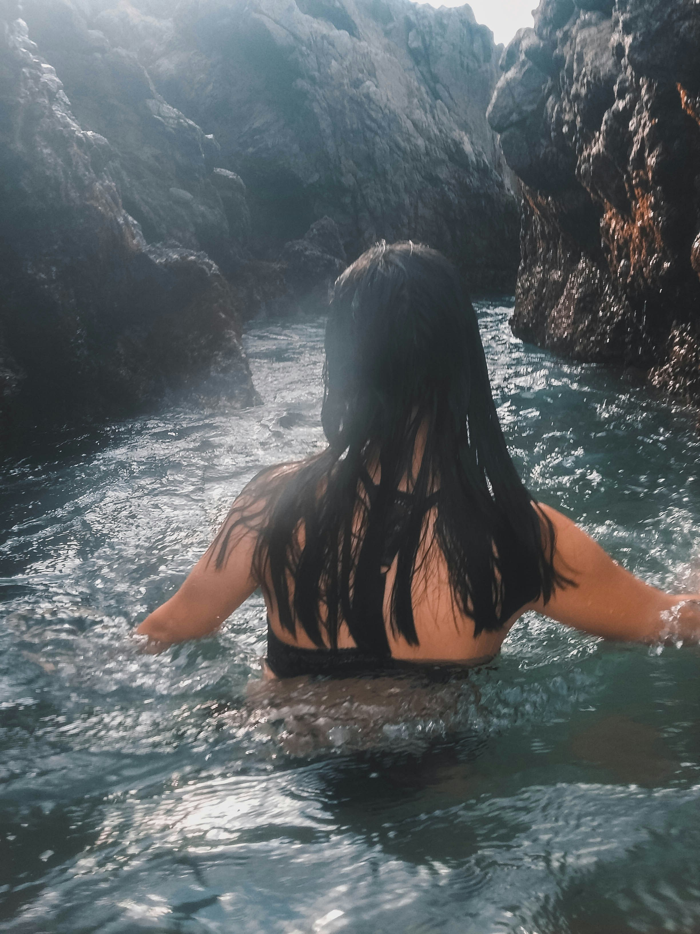 A woman wades through crystal-clear waters surrounded by rugged rock formations, embodying a serene connection with nature.