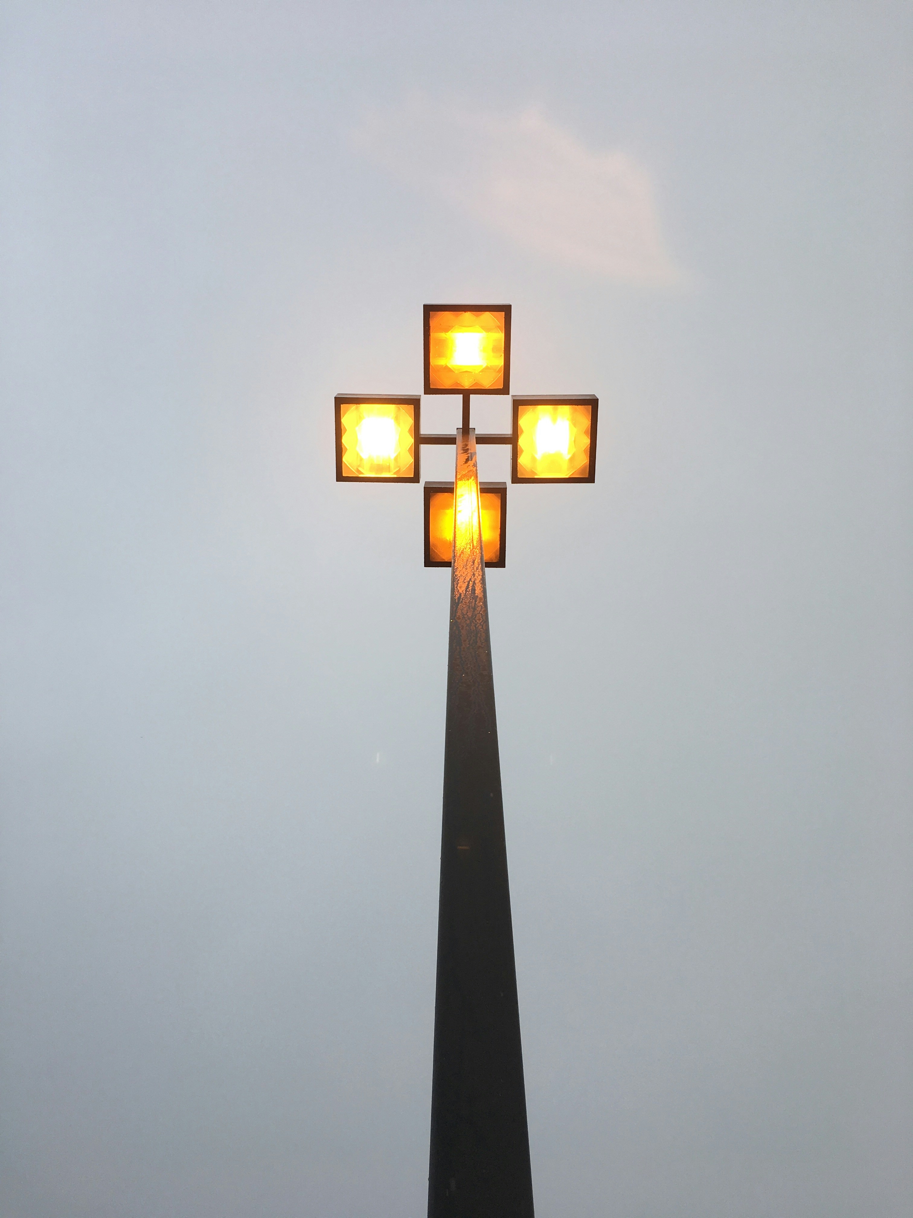 A modern streetlight with four glowing squares against a cloudy sky, showcasing a unique upward perspective.
