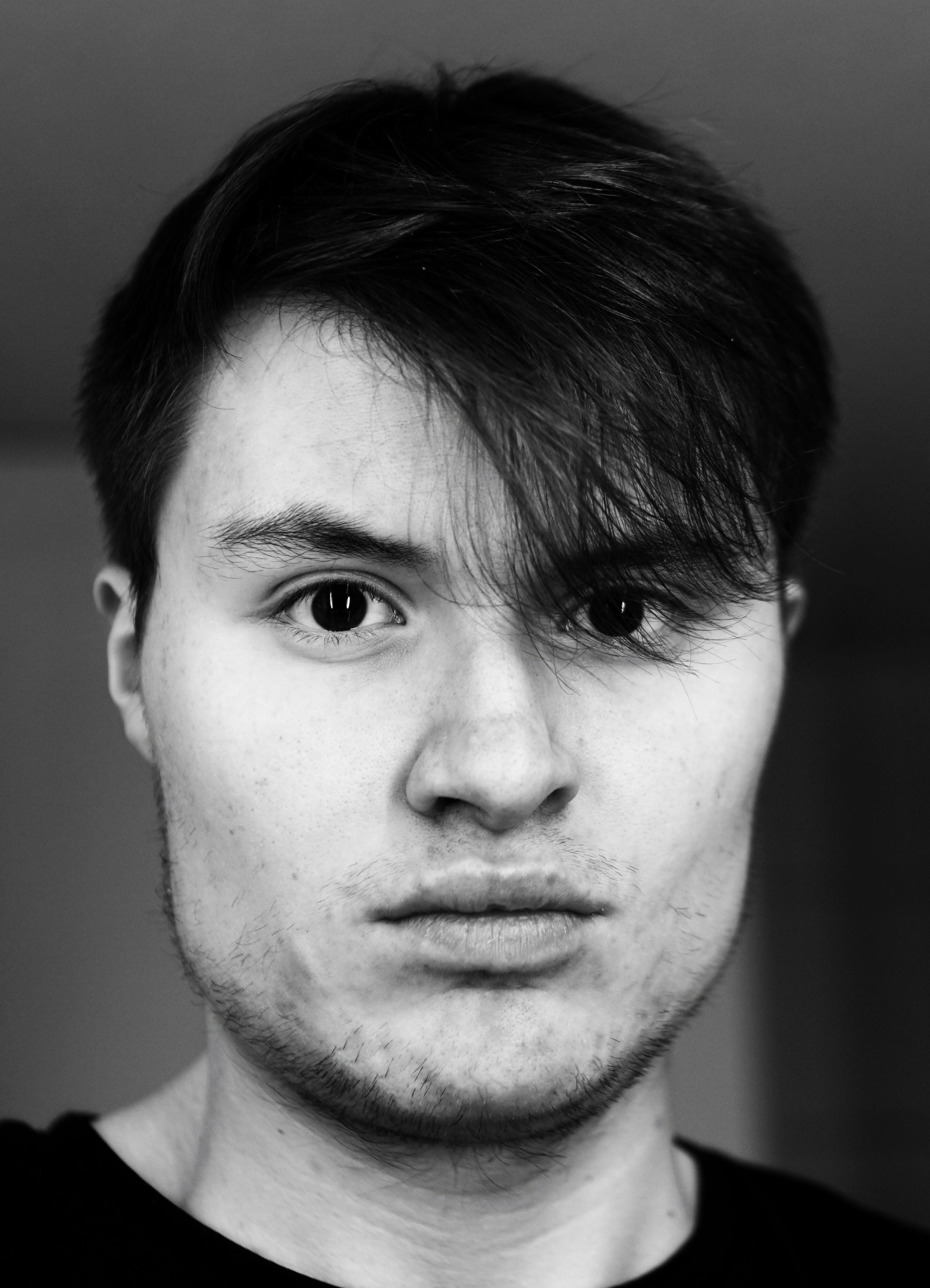 A close-up portrait in black and white, capturing a serious expression with tousled hair and striking eyes.