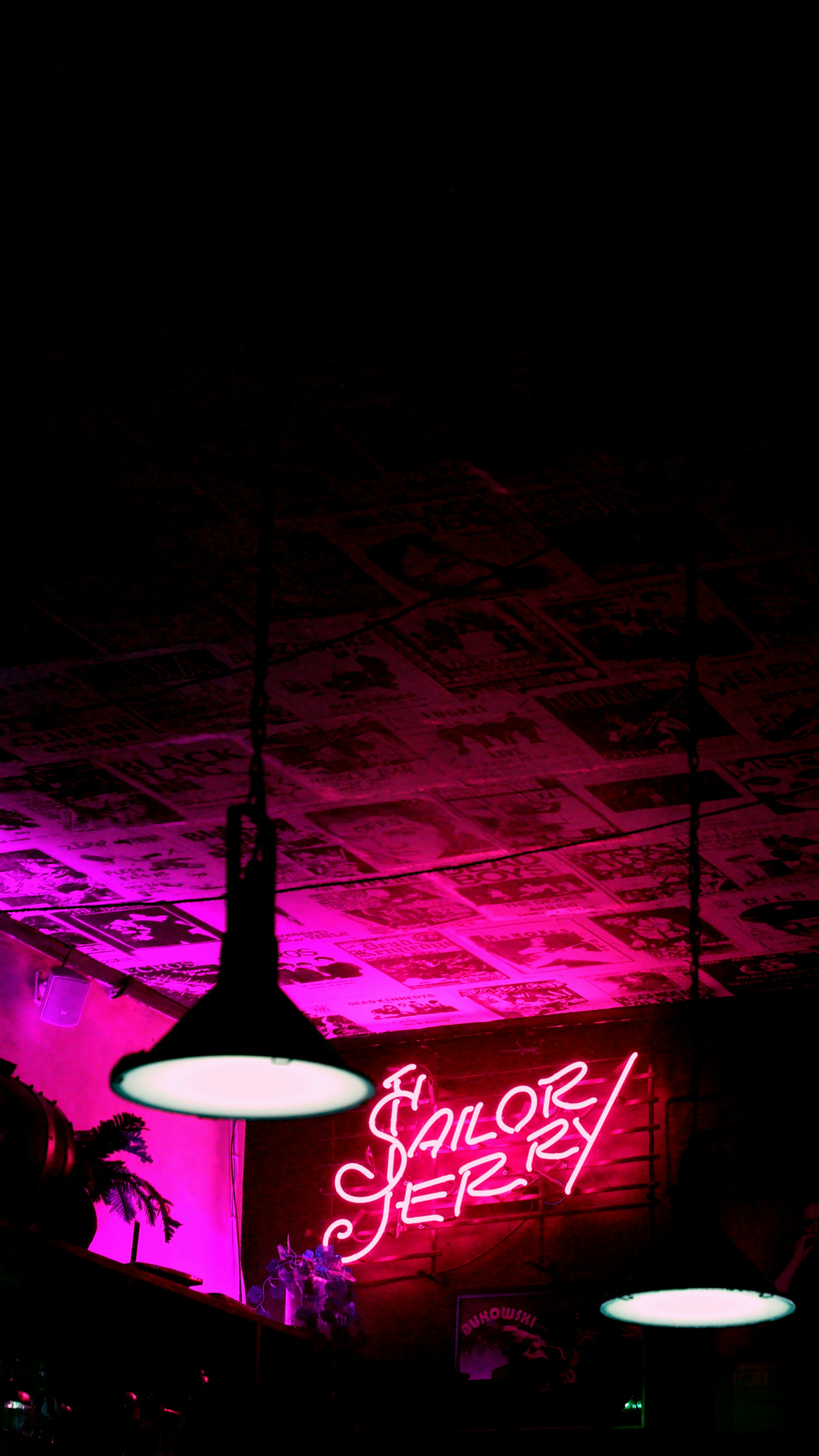Vibrant Sailor Jerry neon sign illuminates a dimly lit bar with pink hues.