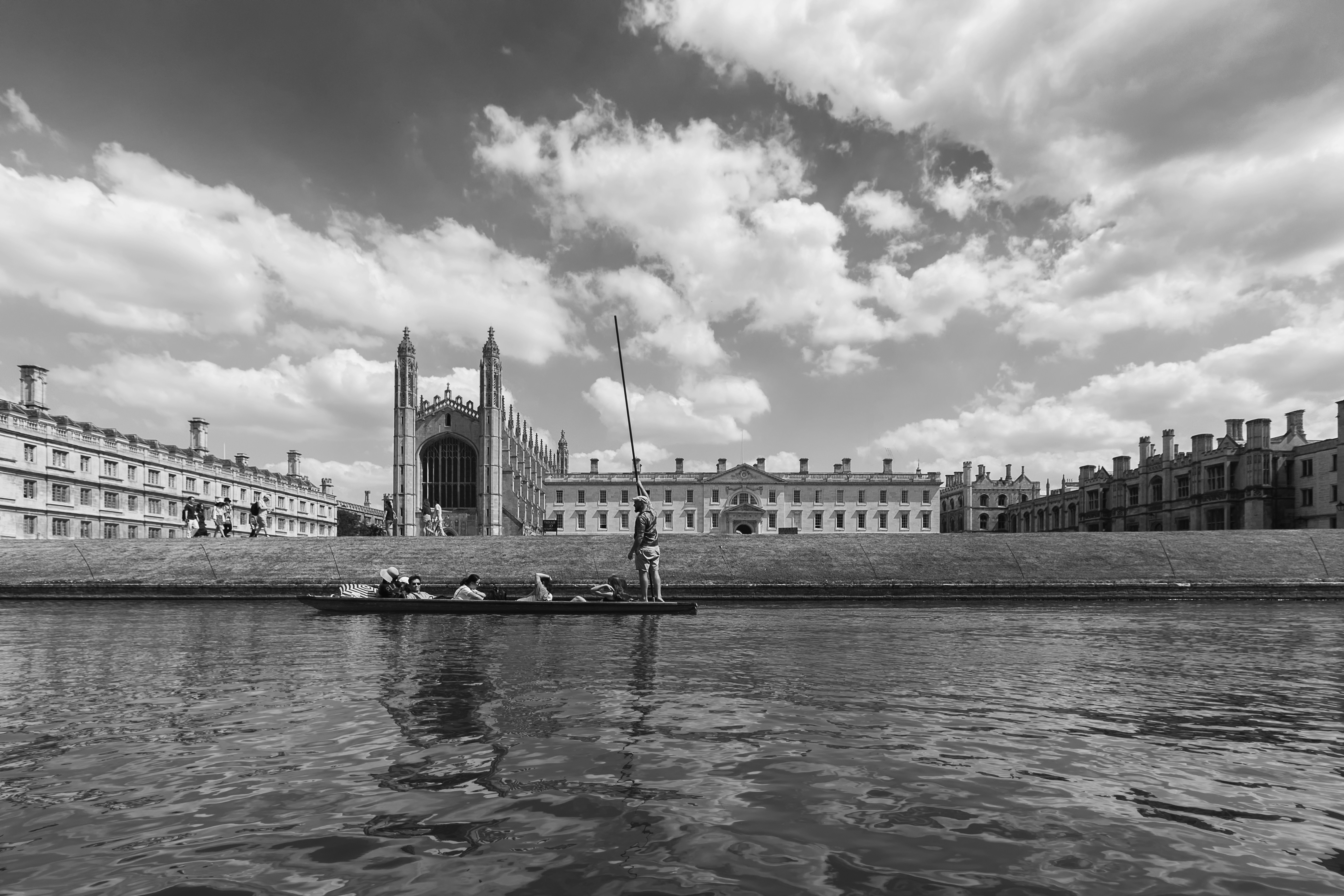 Group in a small boat gliding along a river with a grand historic building in the background under a partly cloudy sky.