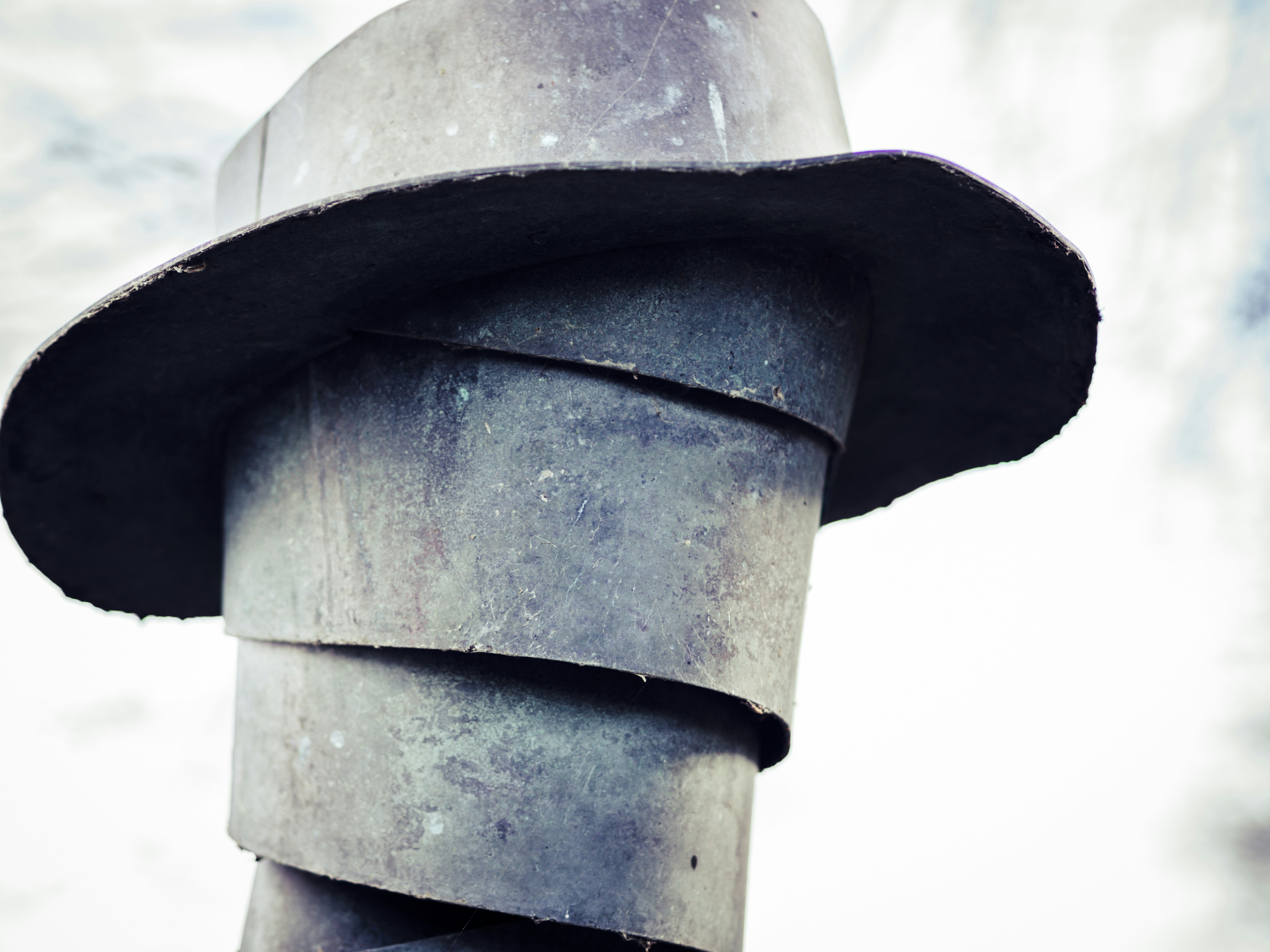 Abstract sculpture resembling a figure with a wide-brimmed hat, showcasing intricate metal layering and weathered textures.