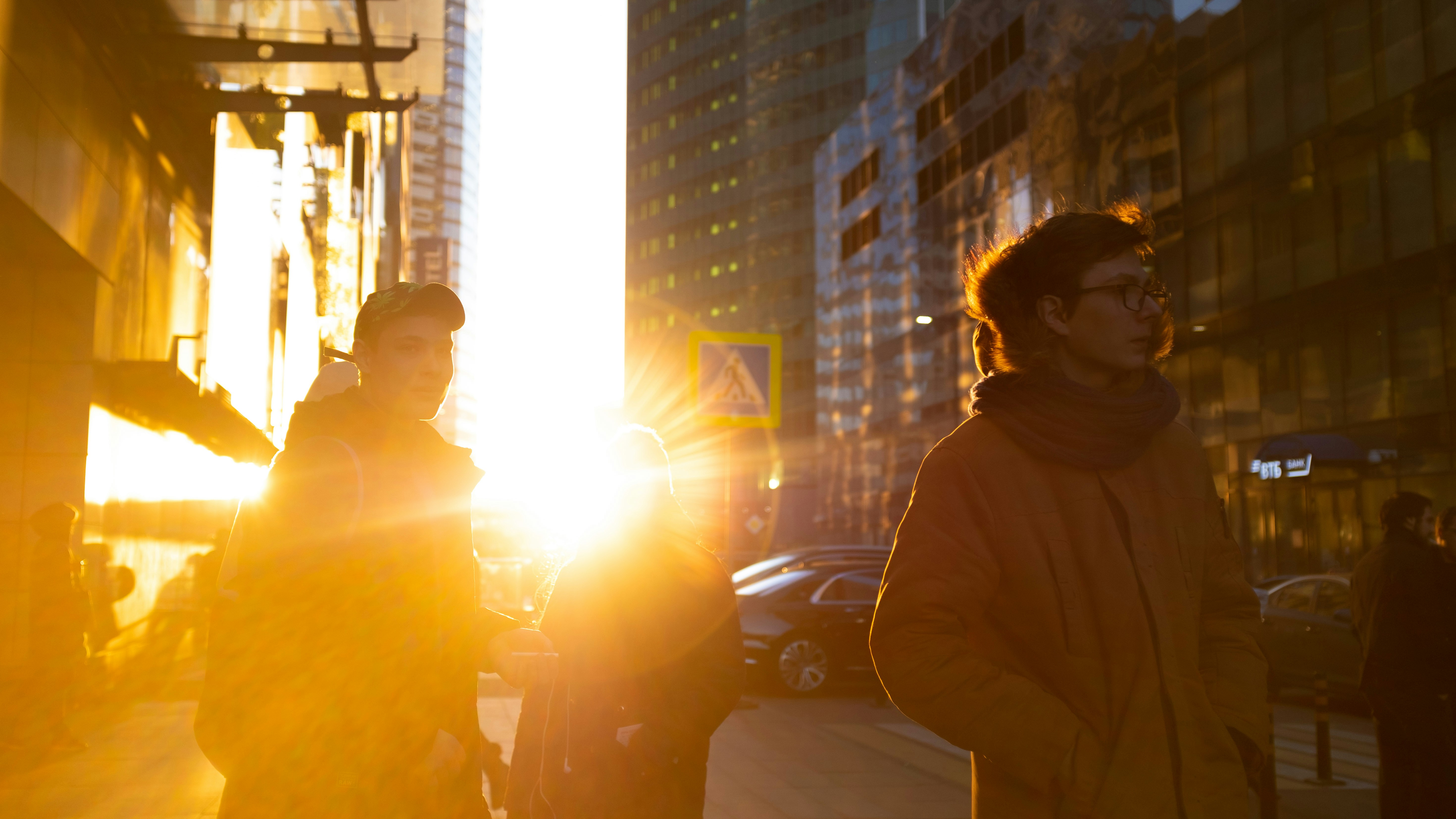 Silhouetted pedestrians walking against a bright sunrise between city skyscrapers.