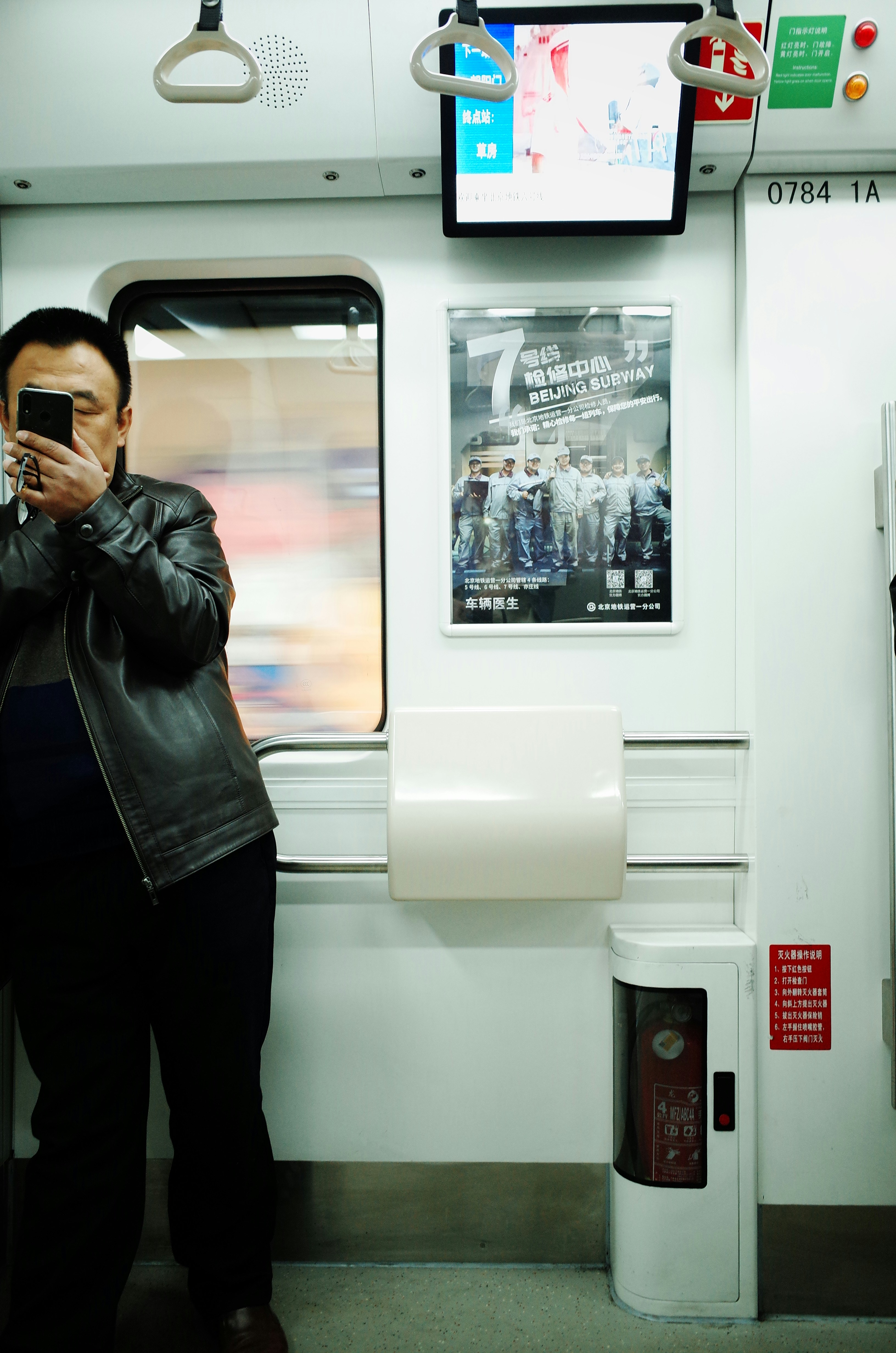 Man with phone reflected in train cabin window, leather jacket foreground