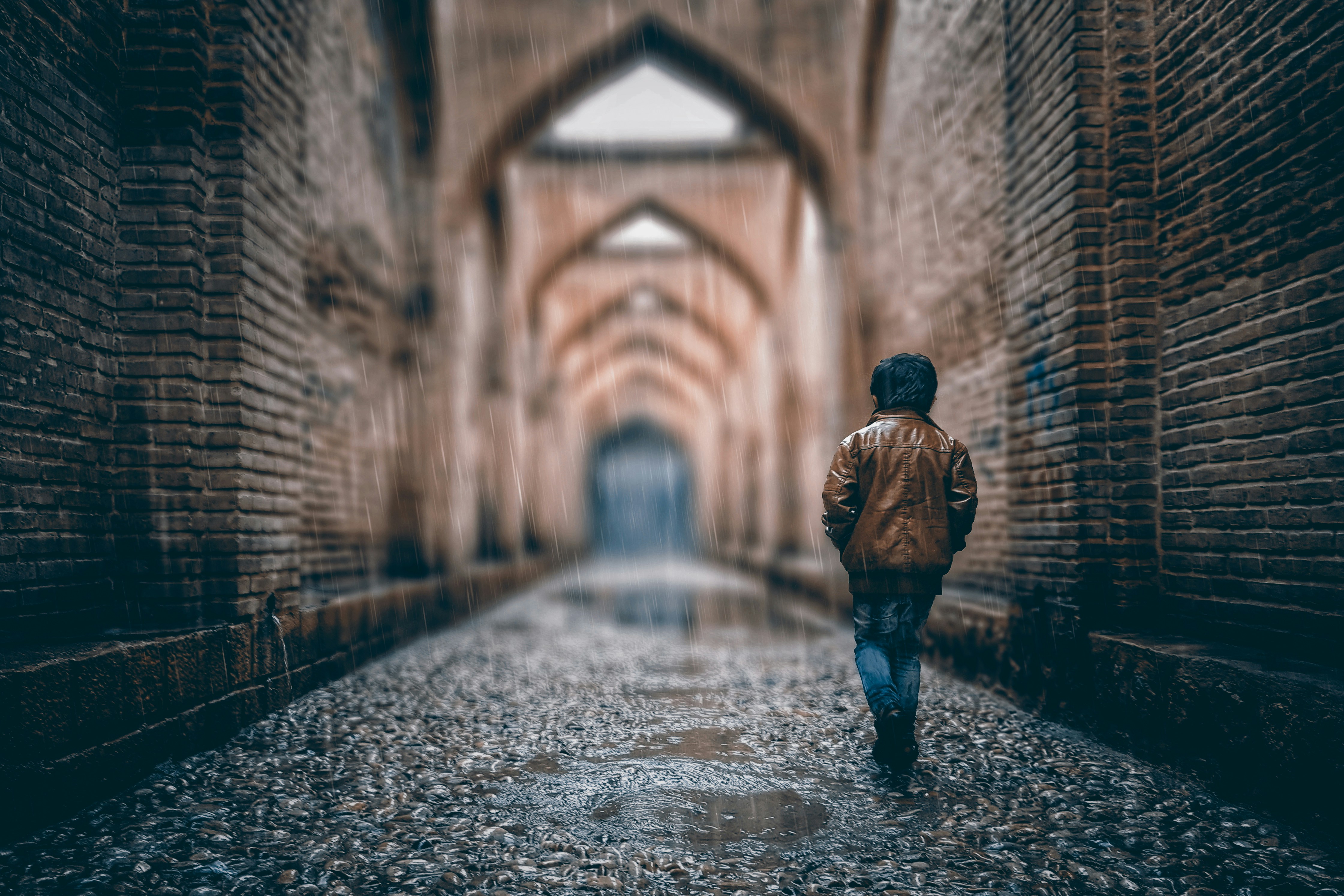 Person walking through an ancient, arched corridor with stone walls and a pebbled path.