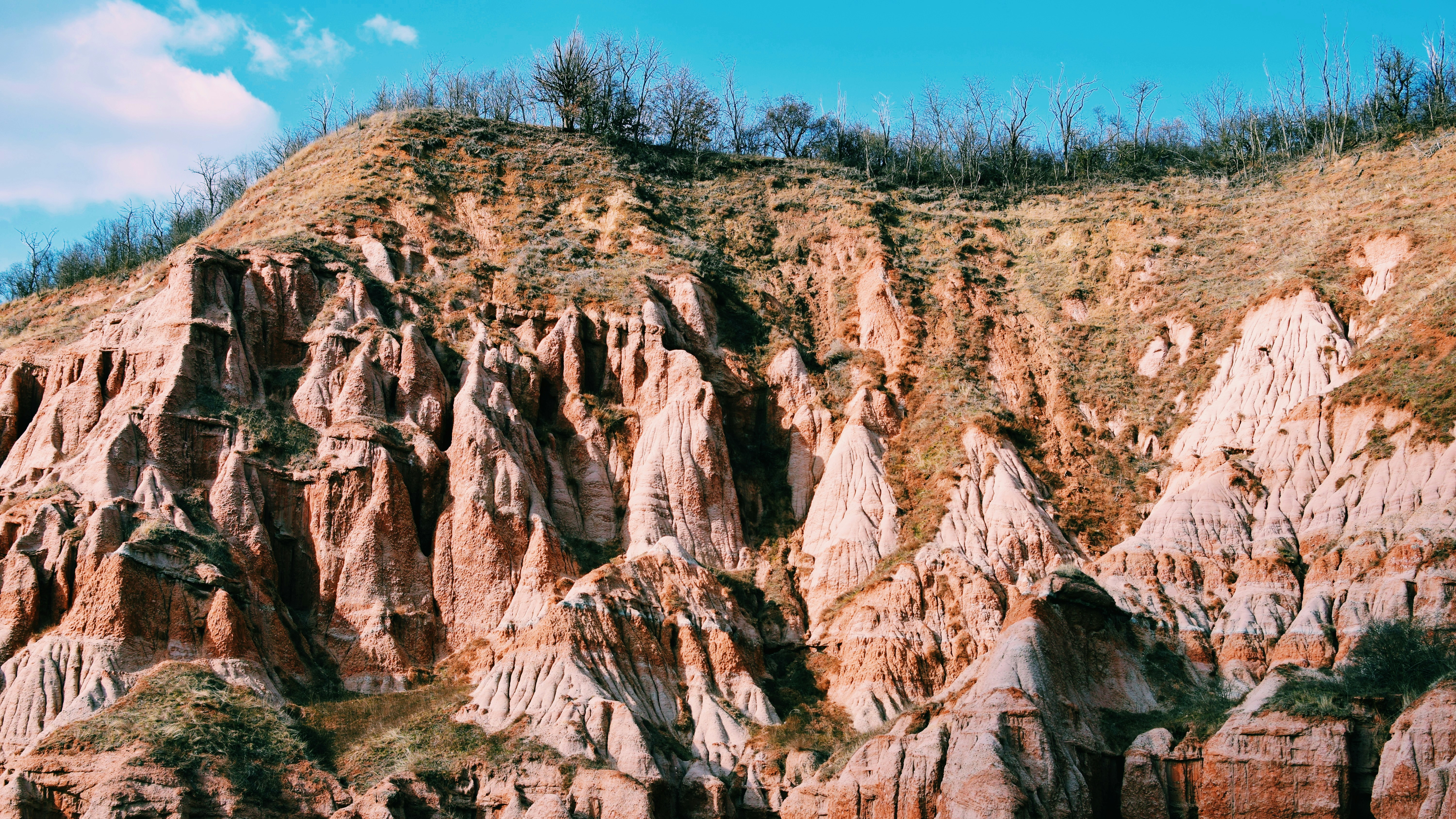 Rugged cliff face with striking pinkish-brown strata under a bright blue sky; the texture of eroded rock forms dramatic ridges and shadows.