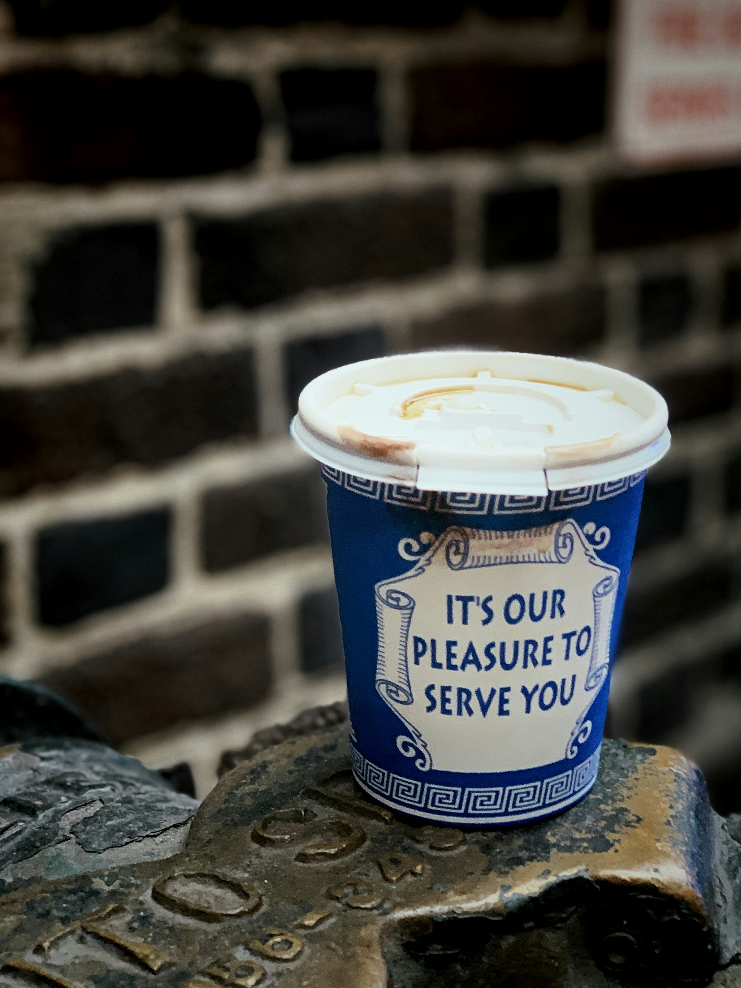 Blue takeaway cup resting on a rusted pedestal against a brick wall