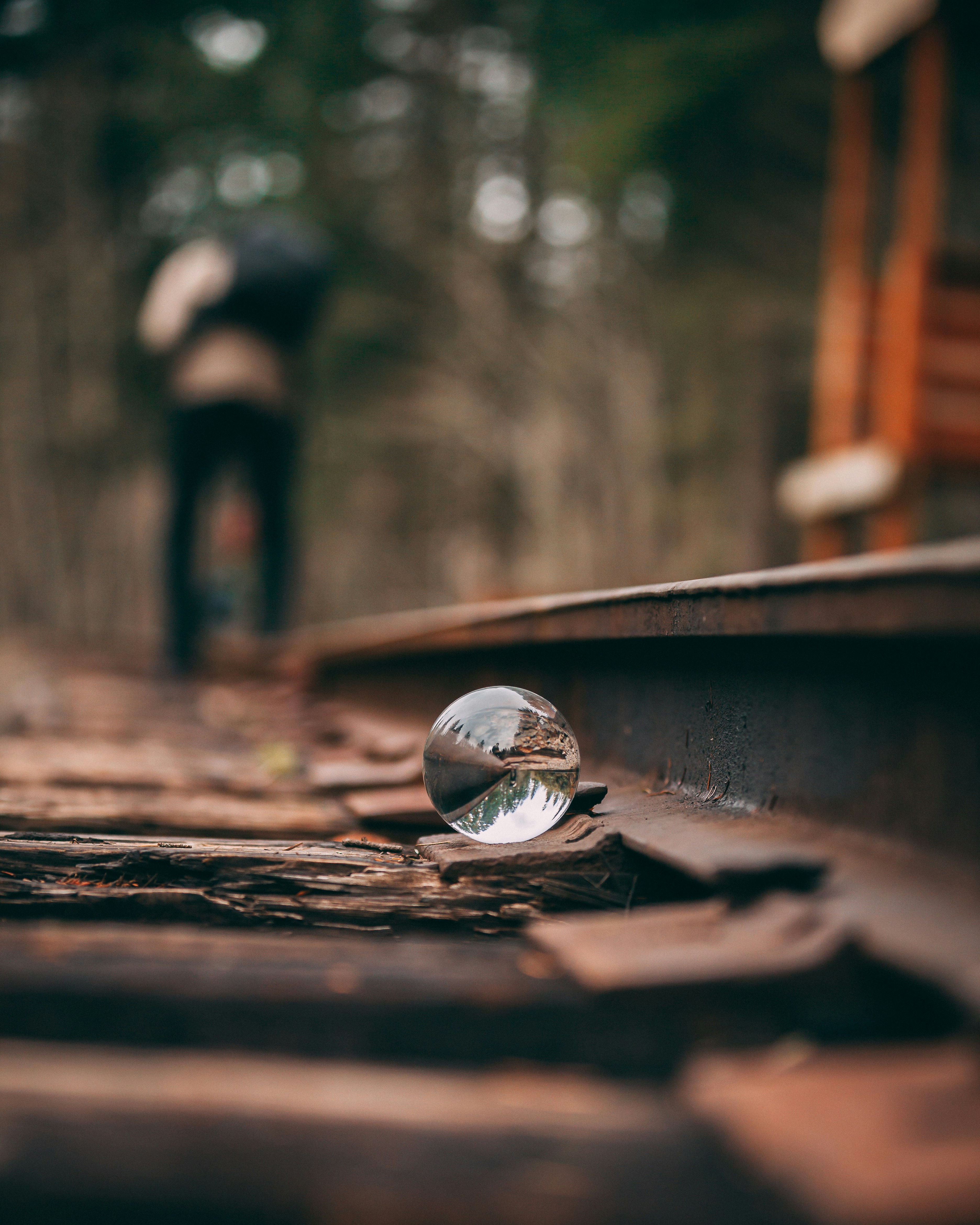 Glass sphere on weathered rails frames a distant figure in a misty forest