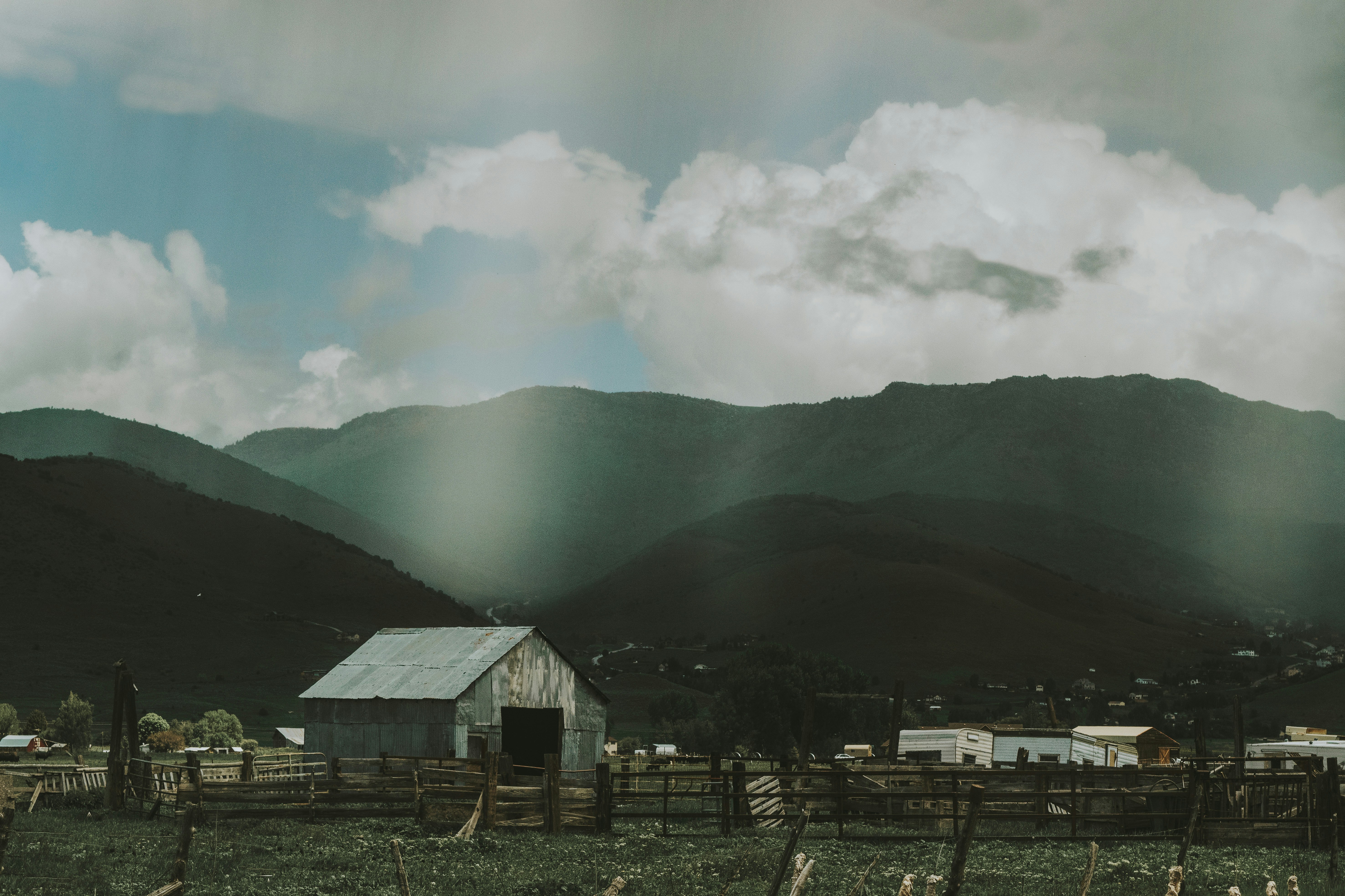 Weathered barn nestled in a lush valley, framed by rolling mountains and a dramatic sky. The scene evokes a sense of tranquility and nostalgia.