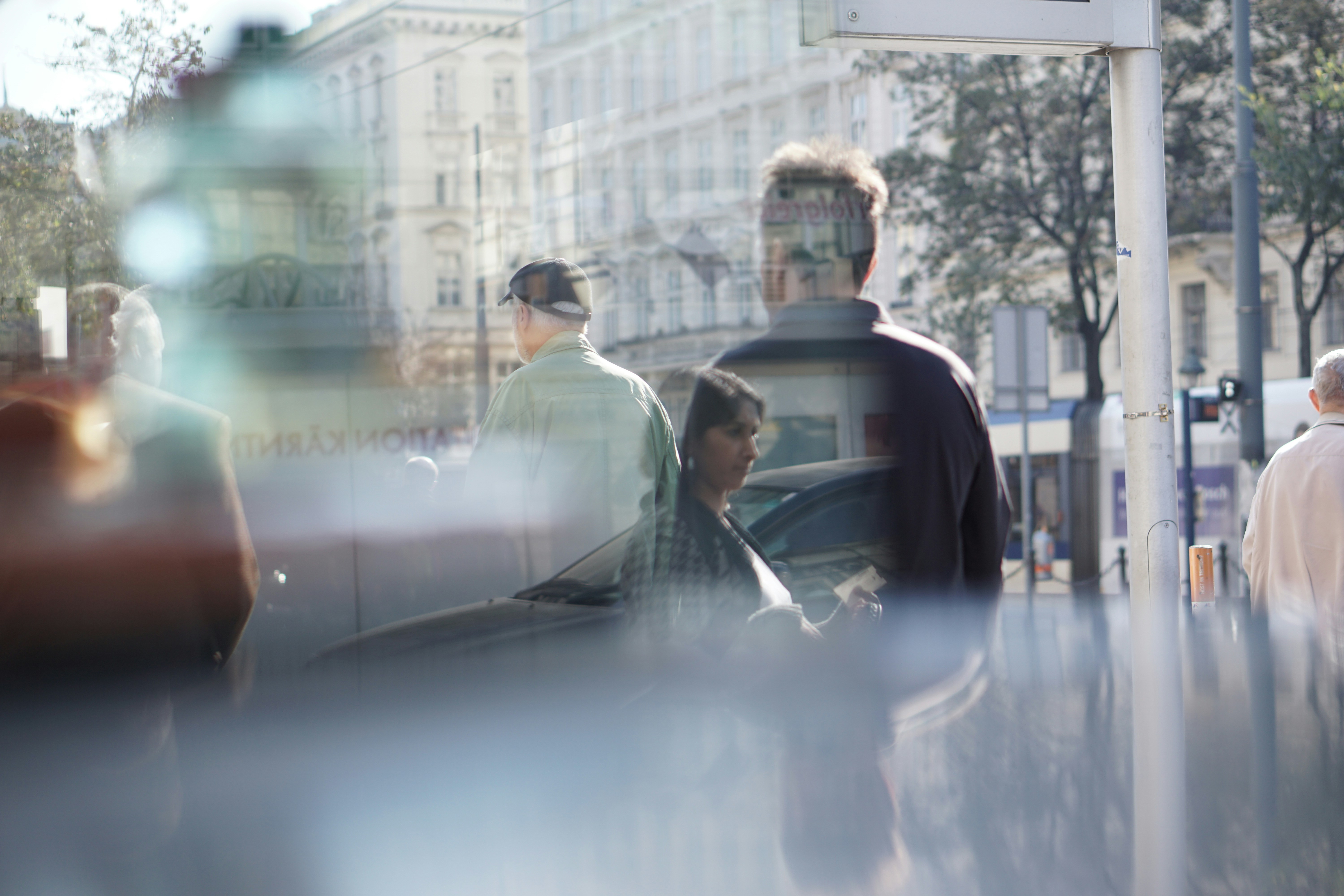 A reflective urban scene capturing pedestrians and city architecture through a glass surface, creating an intriguing interplay of movement and stillness.