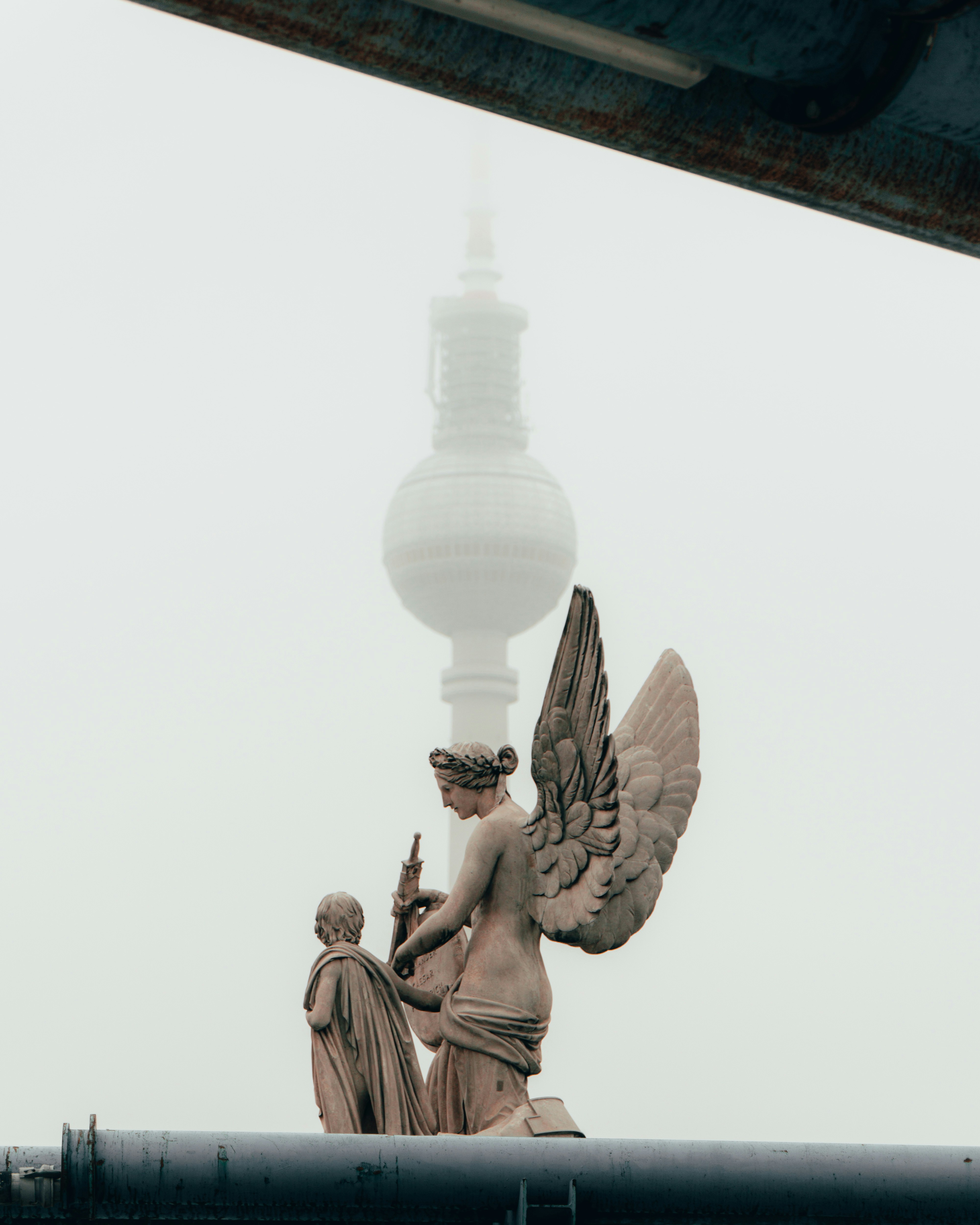 A stone angel statue cradles a child while a distant television tower looms through the mist, creating a serene yet mysterious atmosphere.