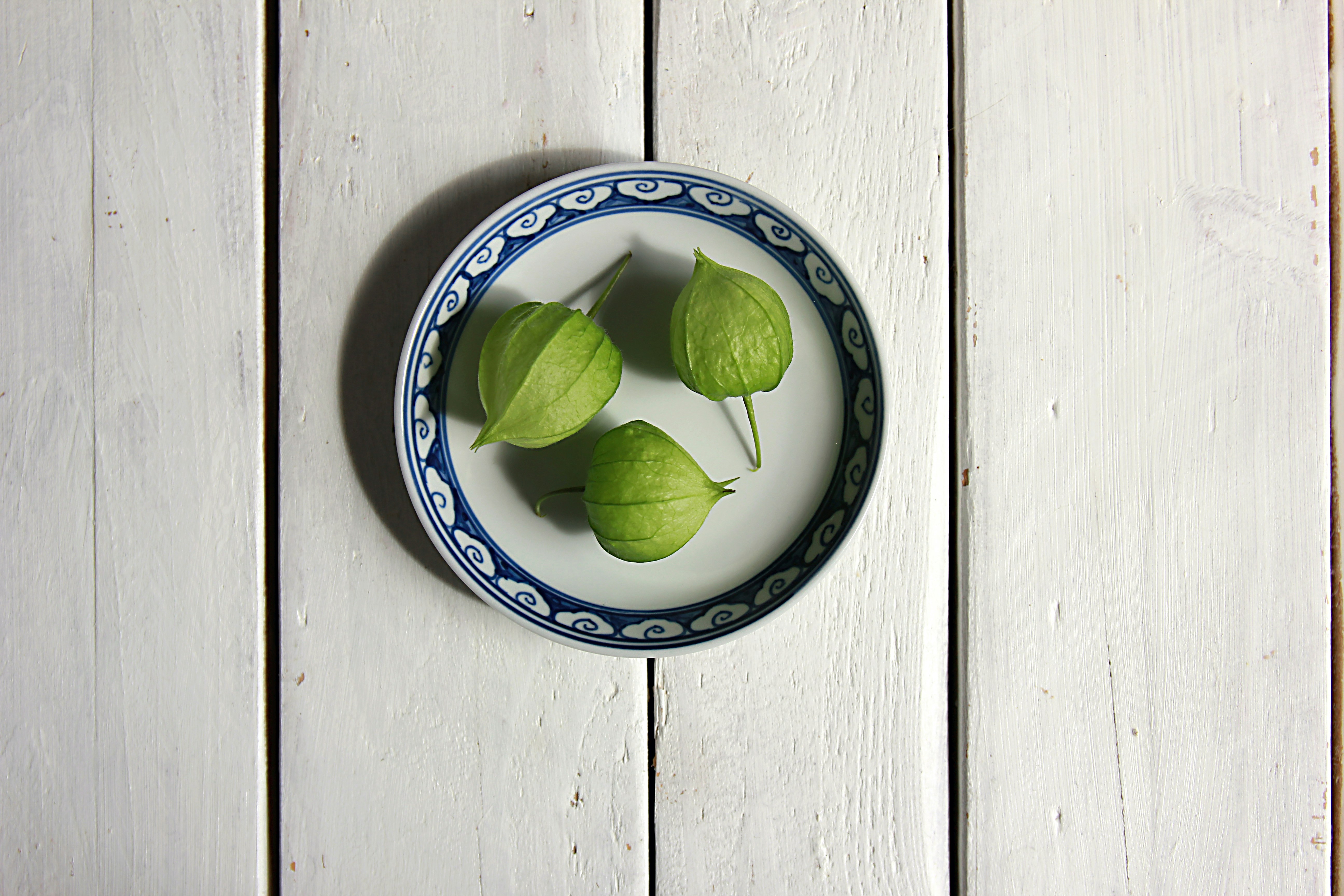 Three green husked fruits arranged on a decorative plate against a rustic wooden backdrop.