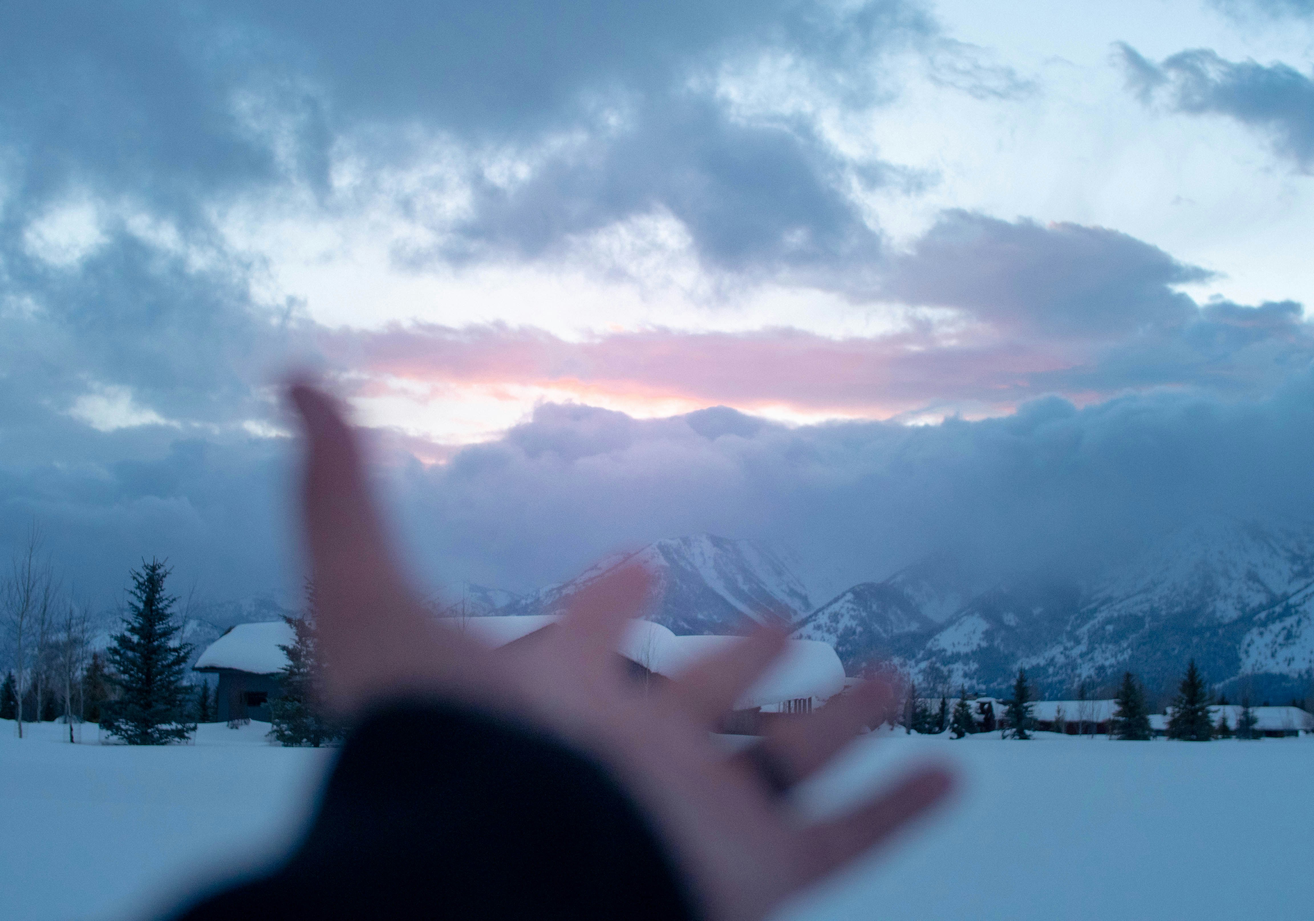 Dawn Reach Over Snow: Blurred Hand Framing Quiet Peaks