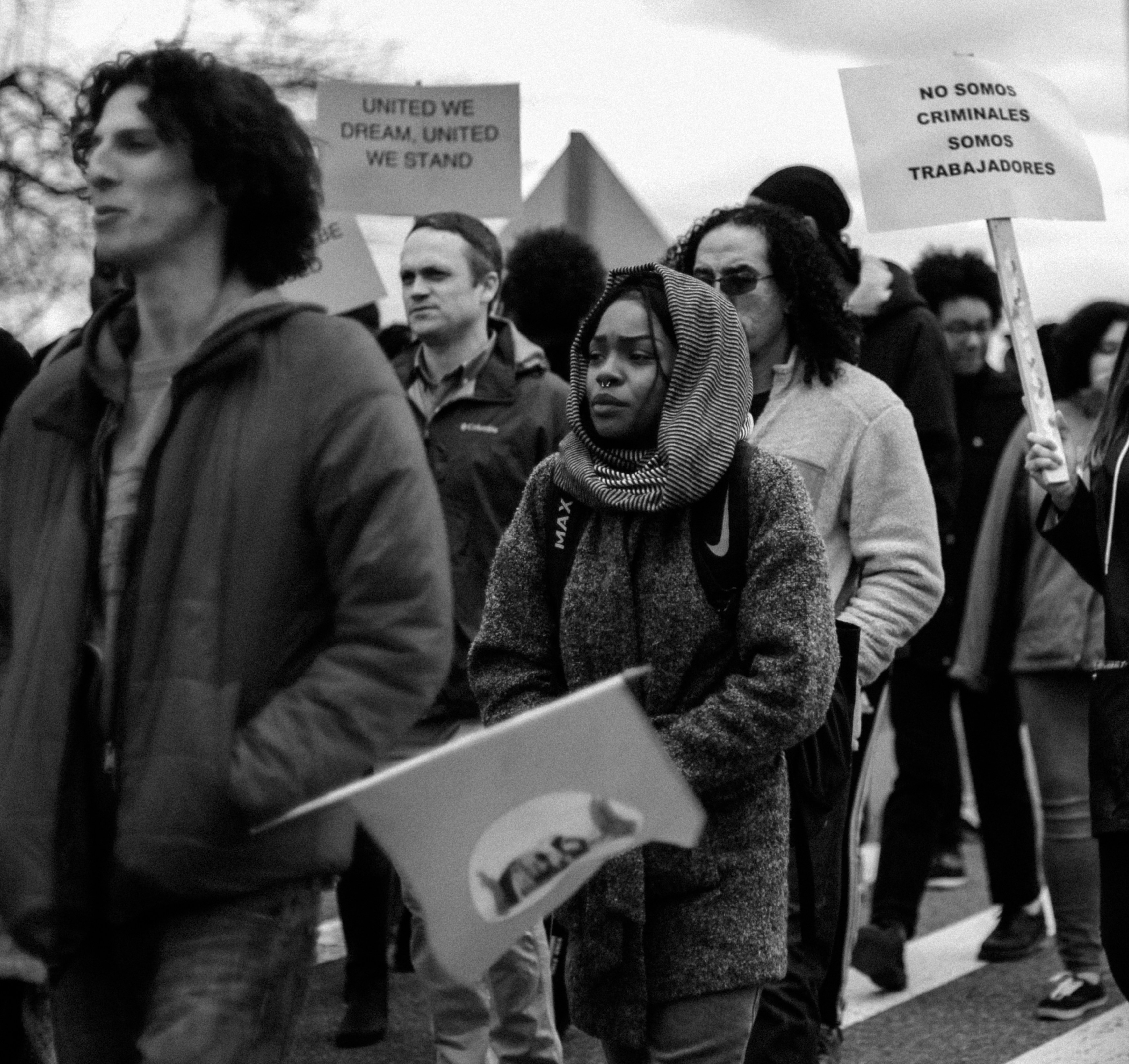 Crowd of diverse individuals marching together, holding signs advocating for rights and unity in a black-and-white setting.
