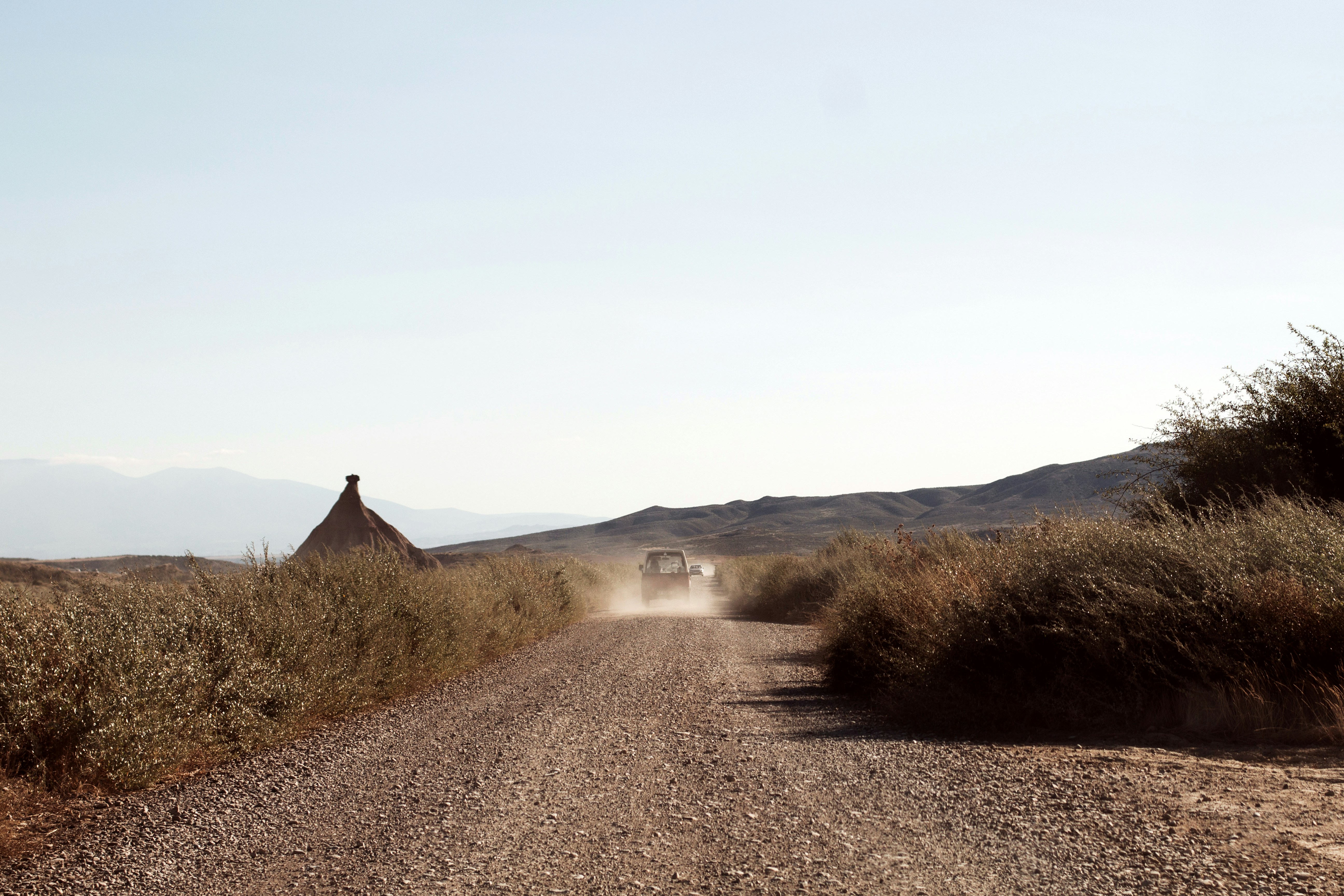 Desert Dust Trail: A Distant Car Traverses the Quiet Gravel Road