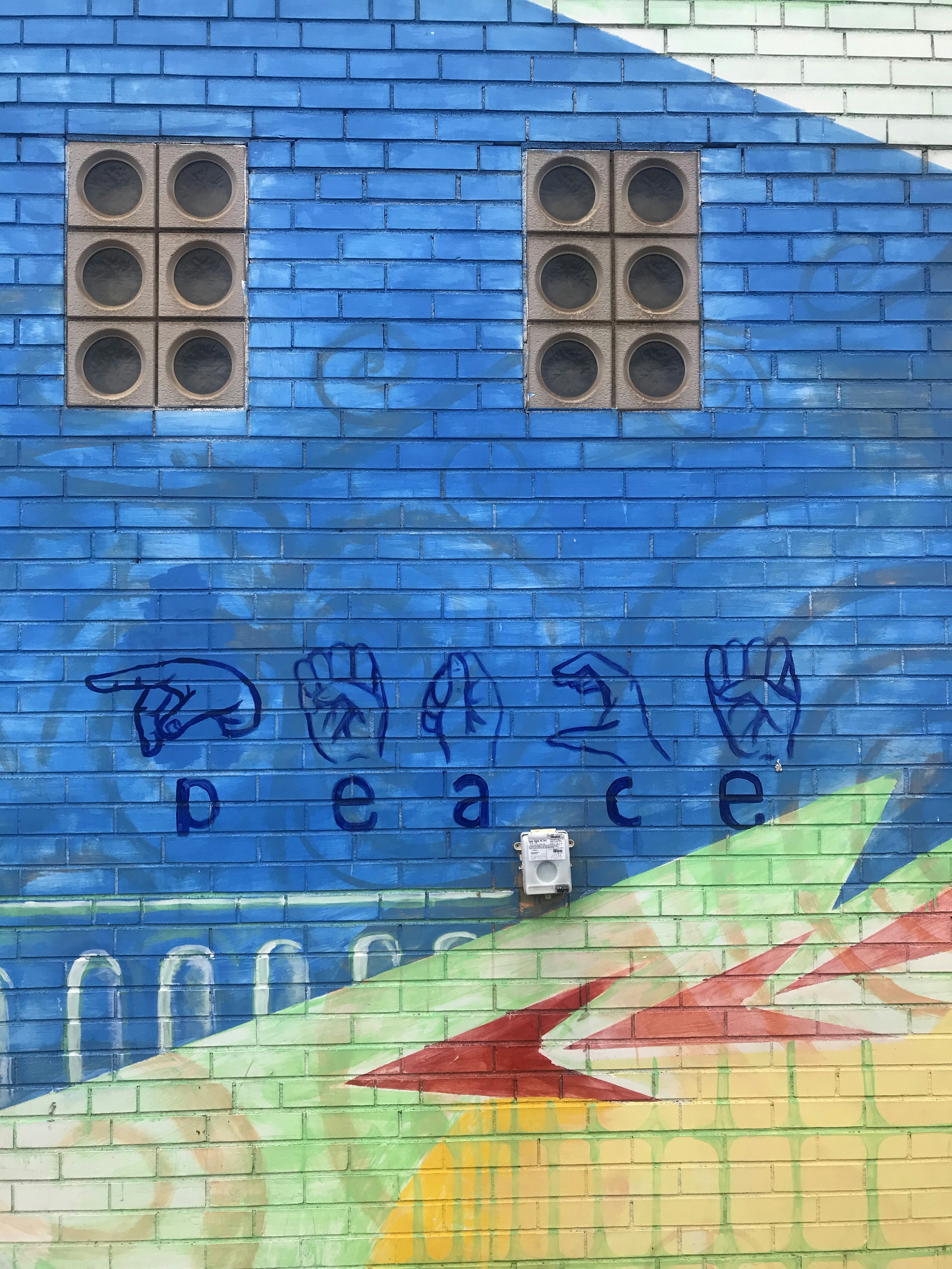 Blue Brick Mosaic: Twin Vent Grilles and a Subtle Peace Graffiti