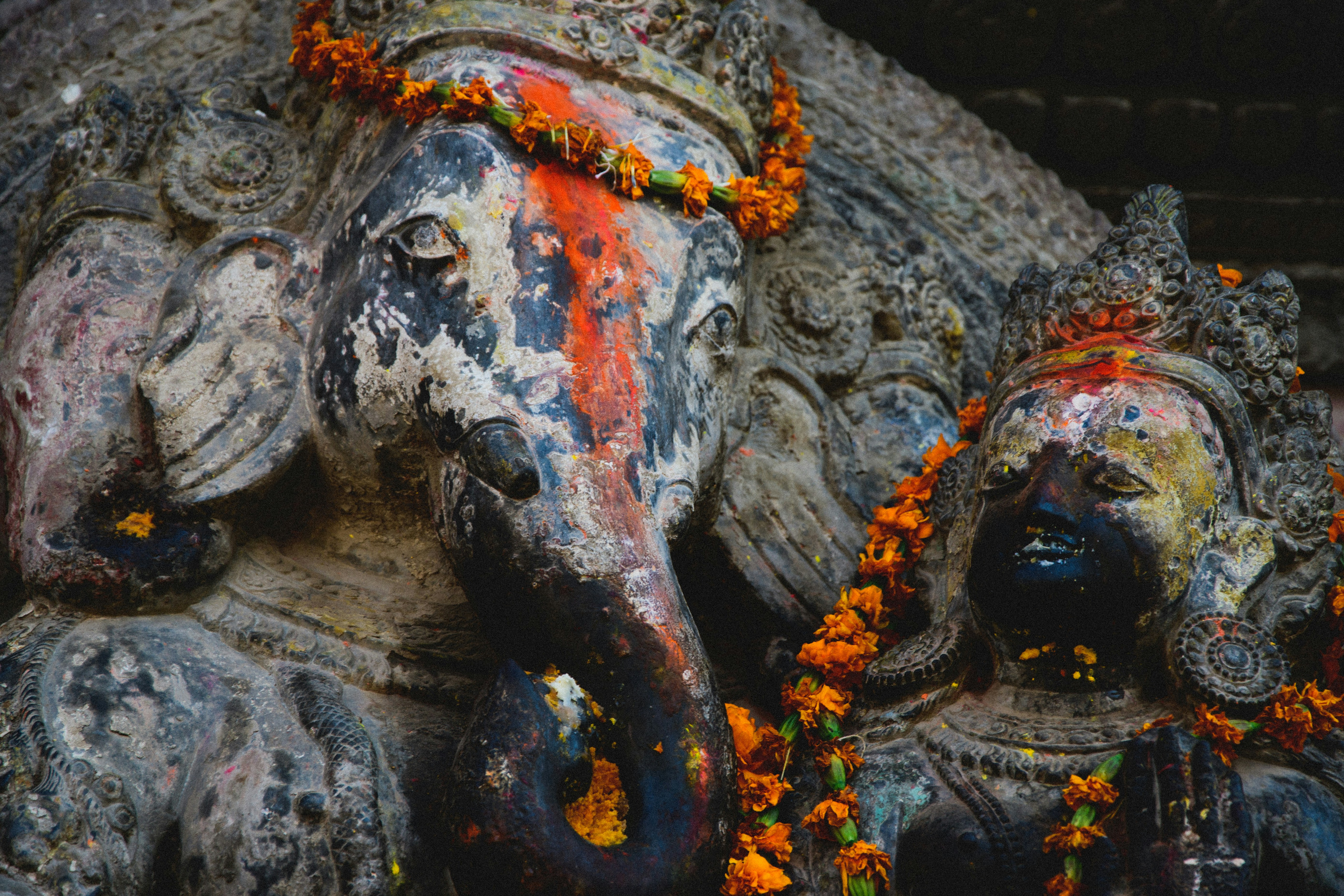 Intricate stone carvings of Ganesh and a female deity adorned with vibrant marigold flowers and ritualistic colors.