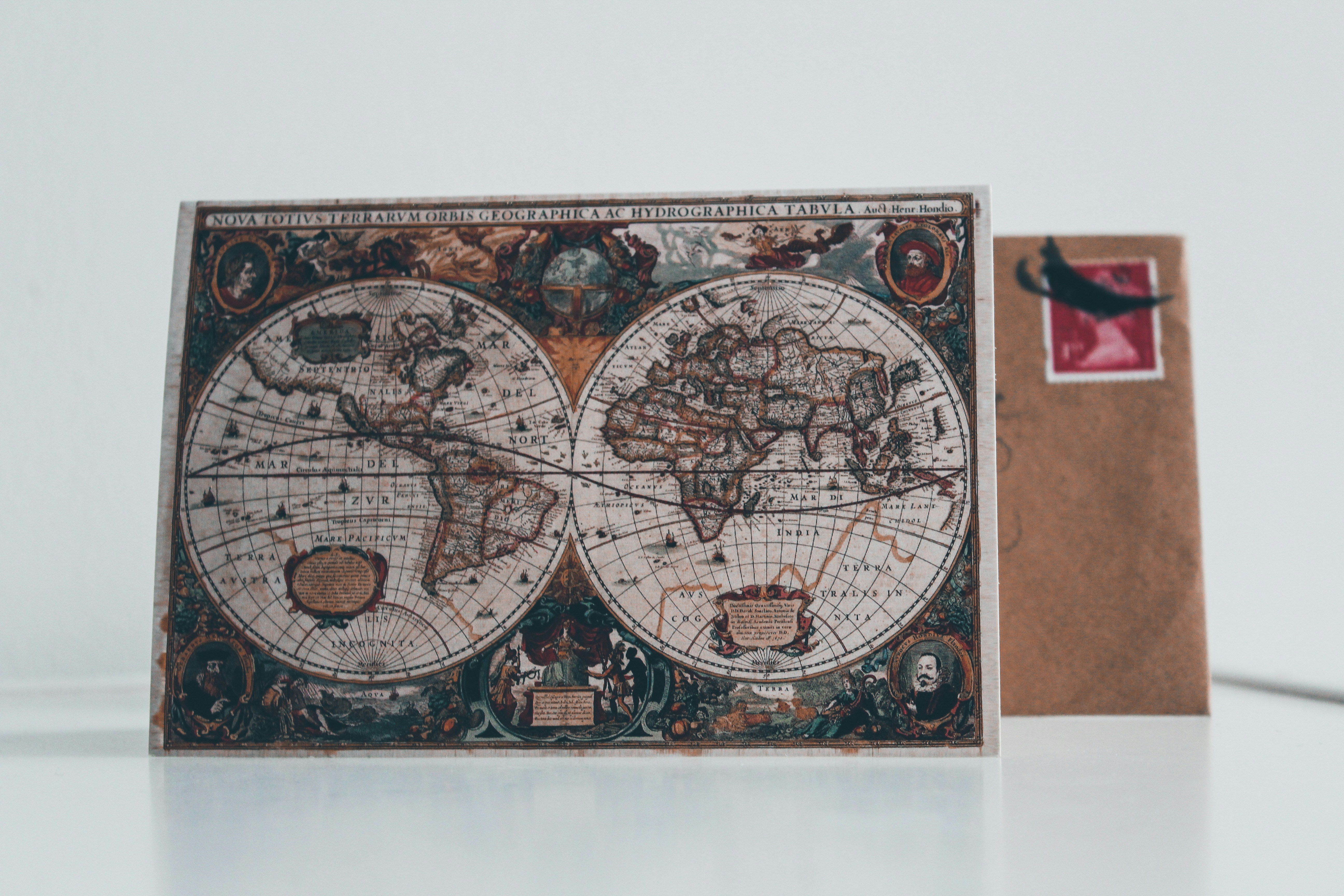 Antique world map featuring intricate designs and geographic details, accompanied by a classic envelope with a postage stamp.