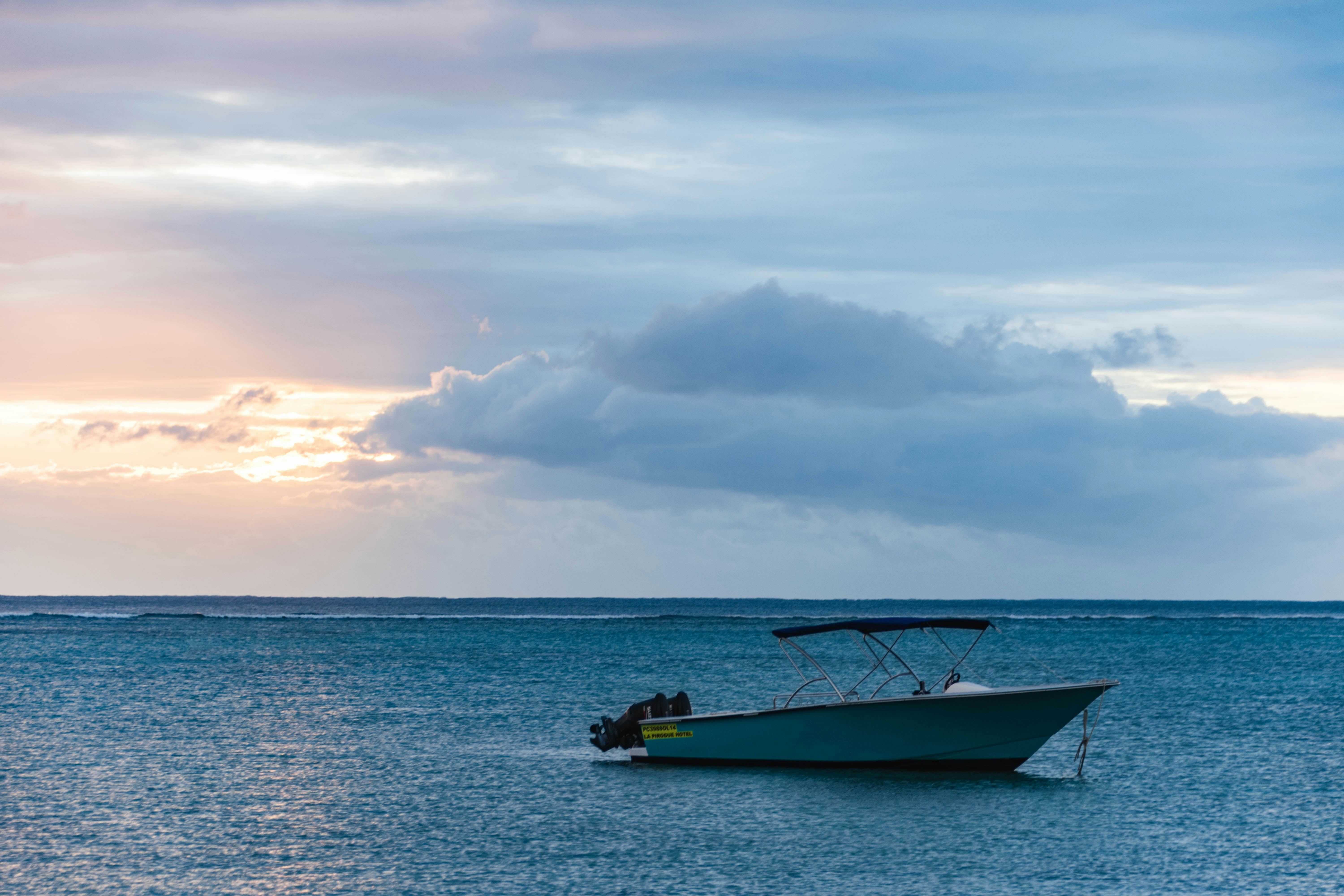 White motorboat anchored on calm sea under a pastel sunset sky.