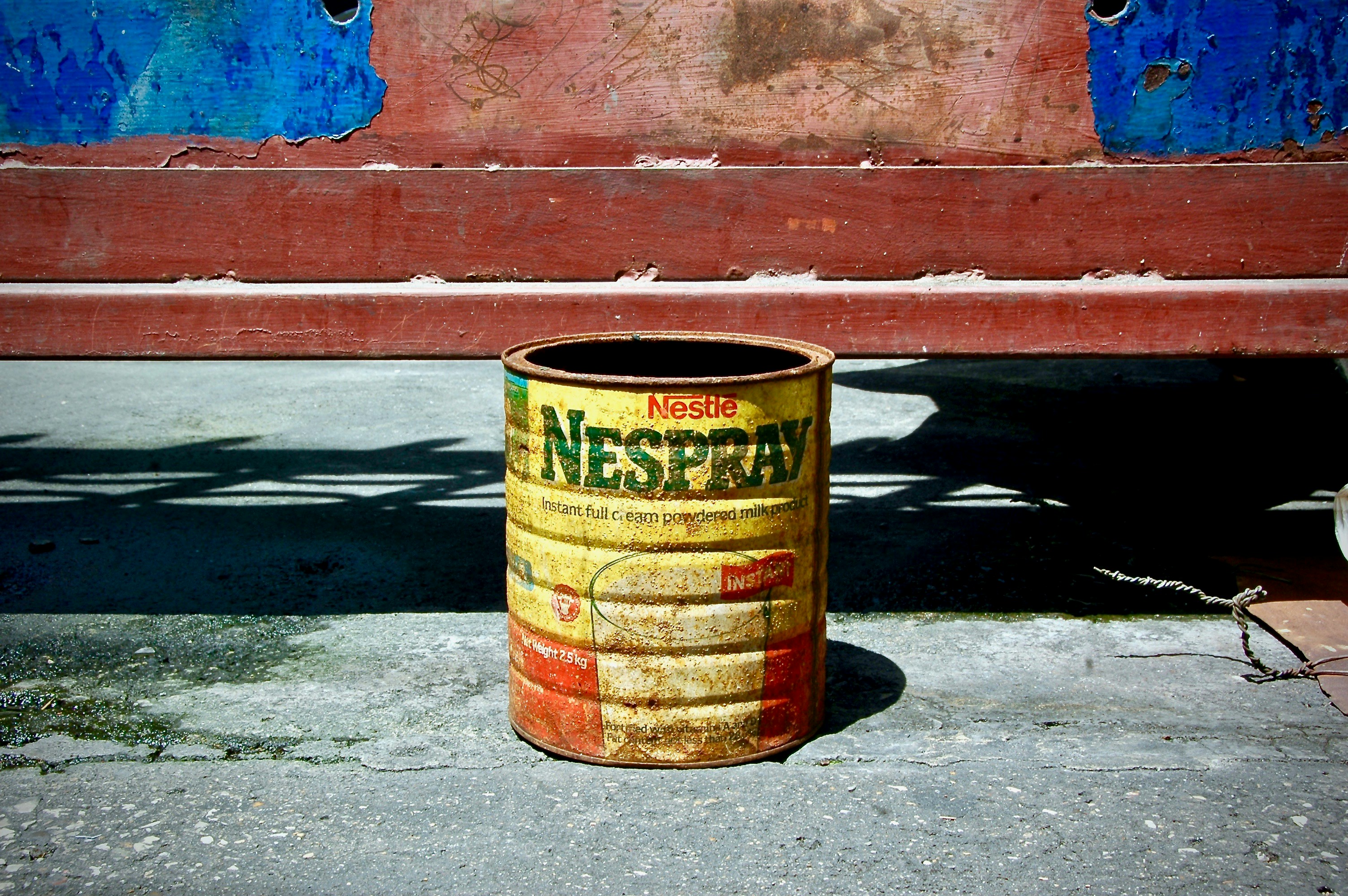 Sun-Baked Nespray Tin: A Rusted Quiet Moment on a Cracked Street