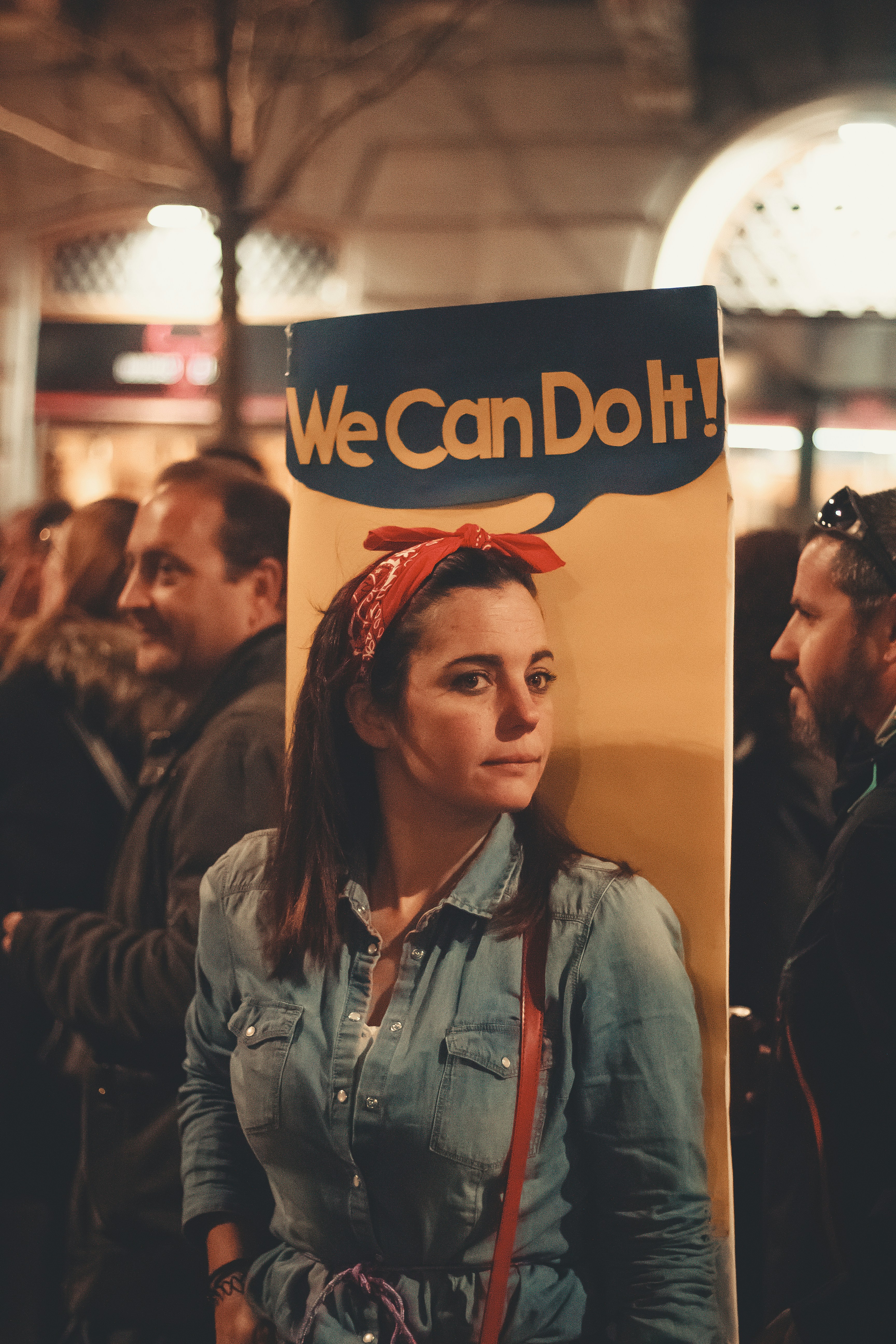 We Can Do It! banner frames a woman as the crowd’s focus at a lively night scene