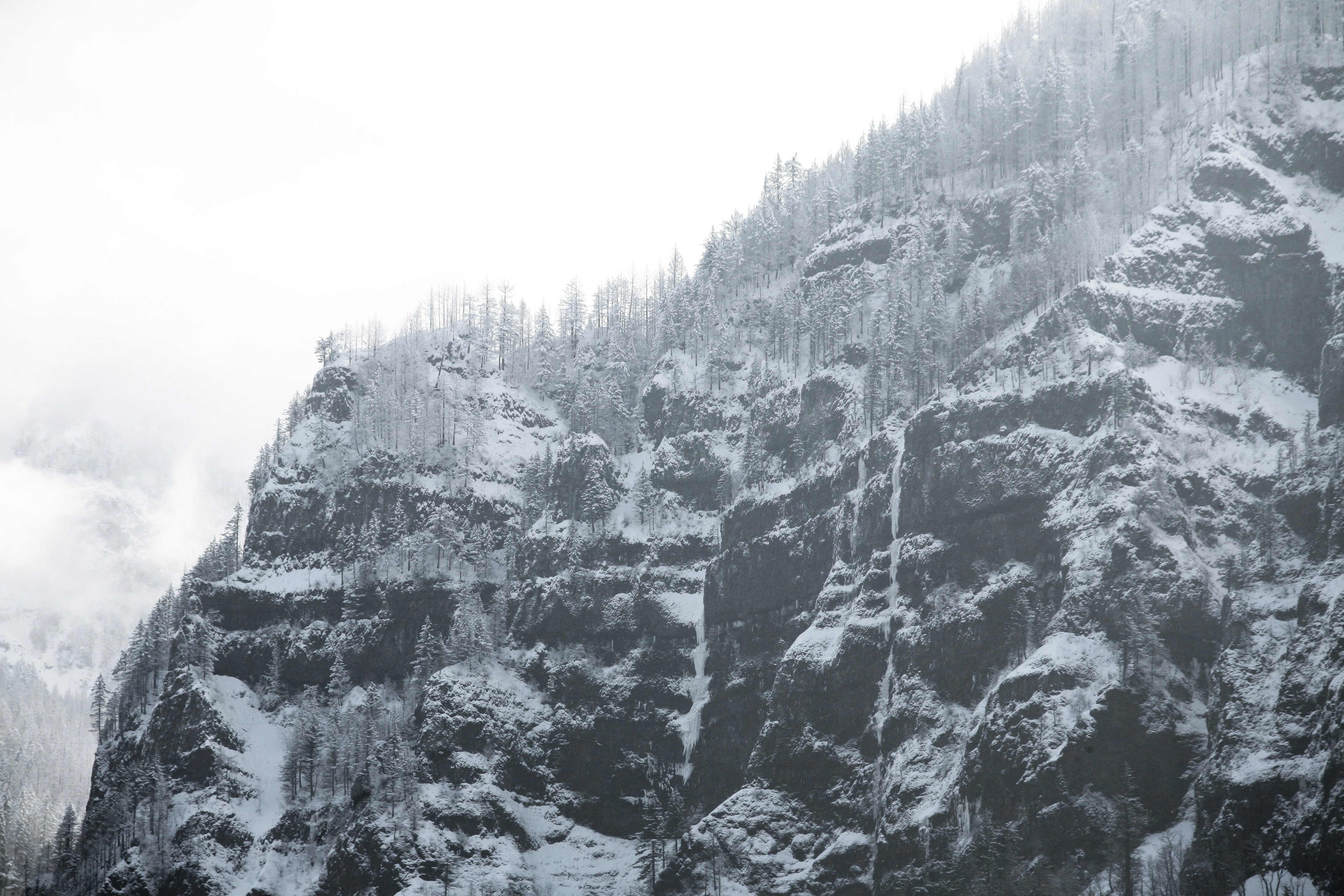 Snow-covered mountain cliffs shrouded in mist, showcasing the rugged beauty of winter's embrace.
