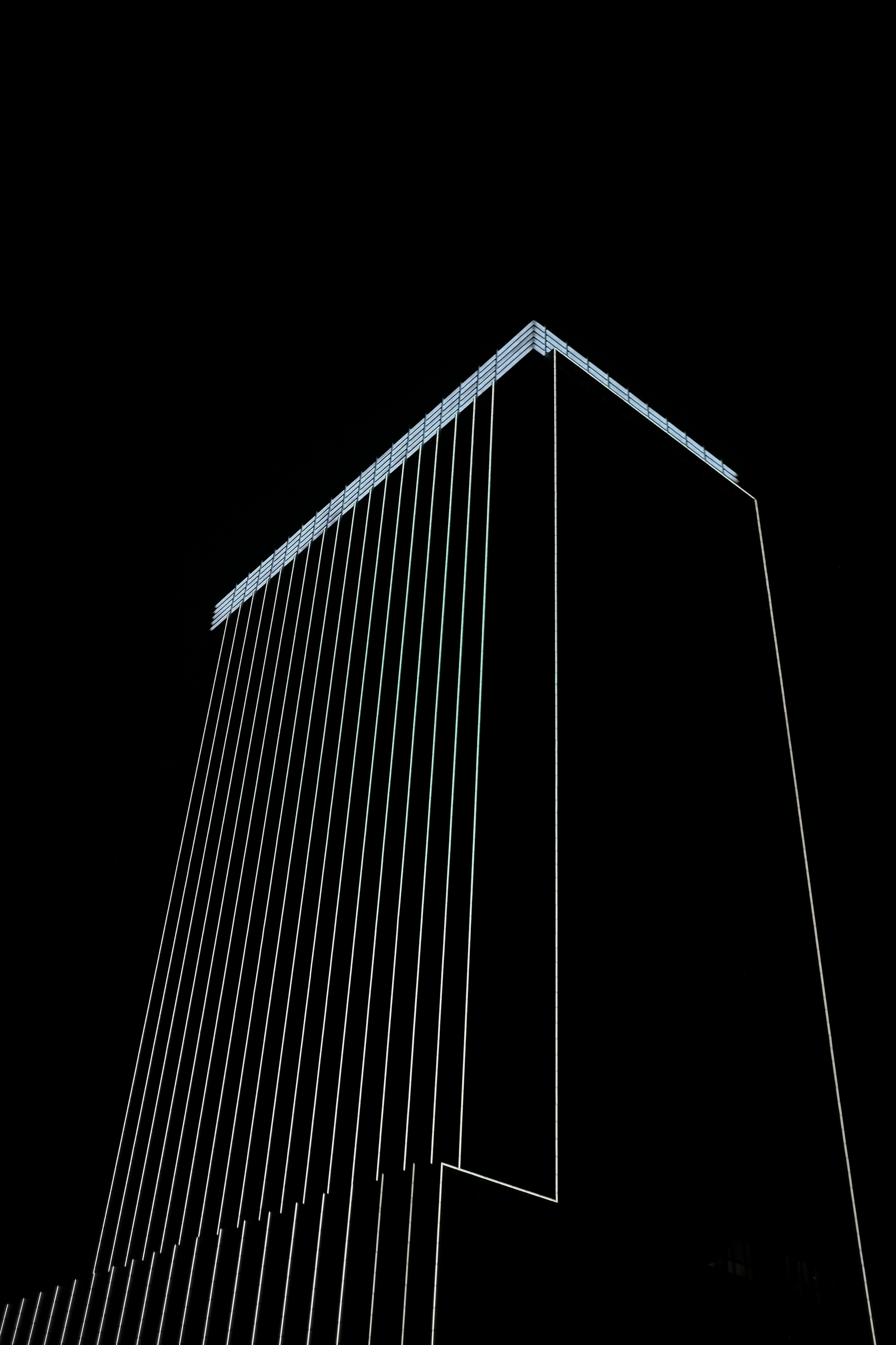A modern skyscraper with sharp lines and illuminated edges, set against a deep black sky.