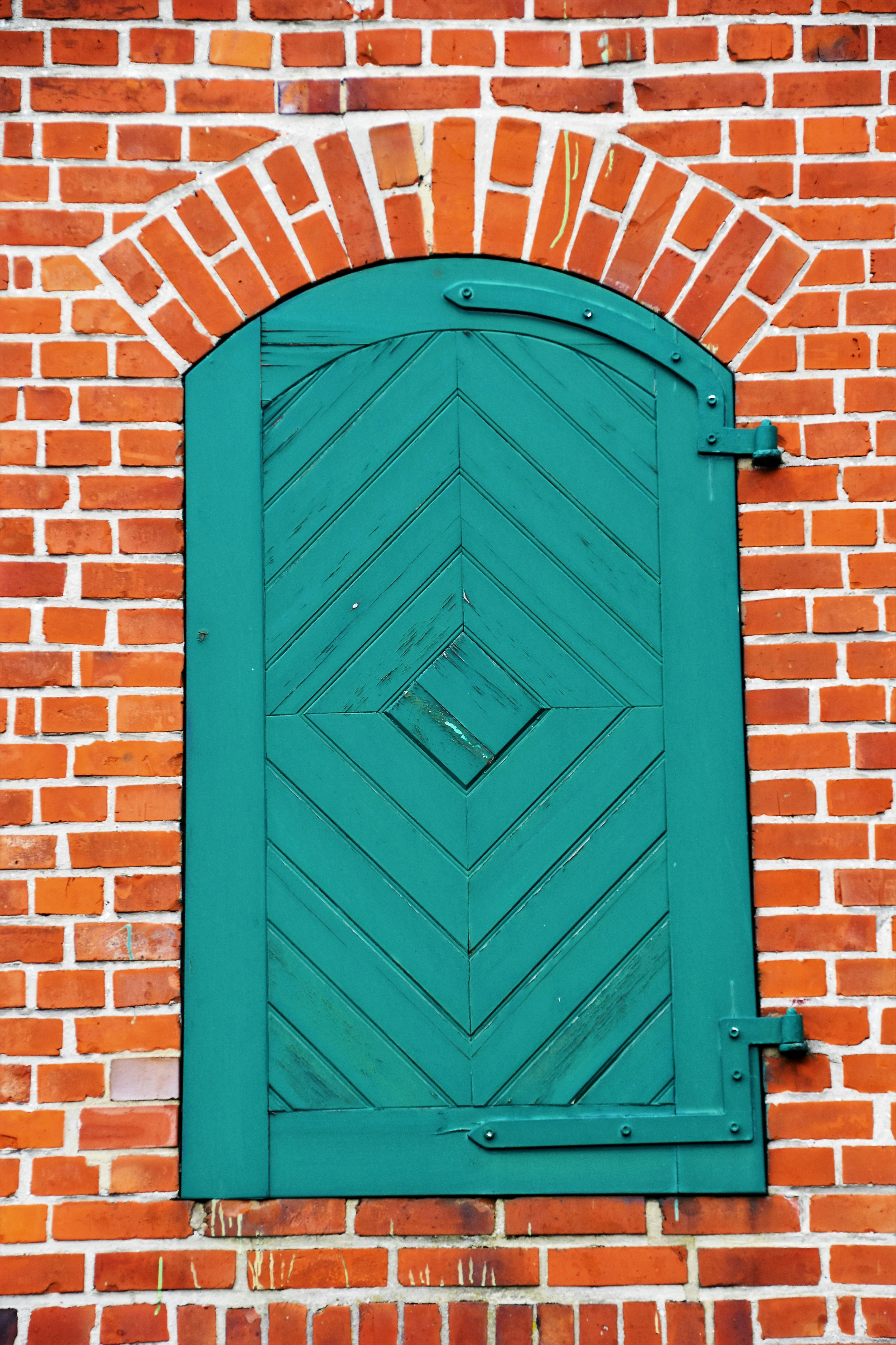 Vintage green wooden door with a diamond pattern set against a textured red brick wall.