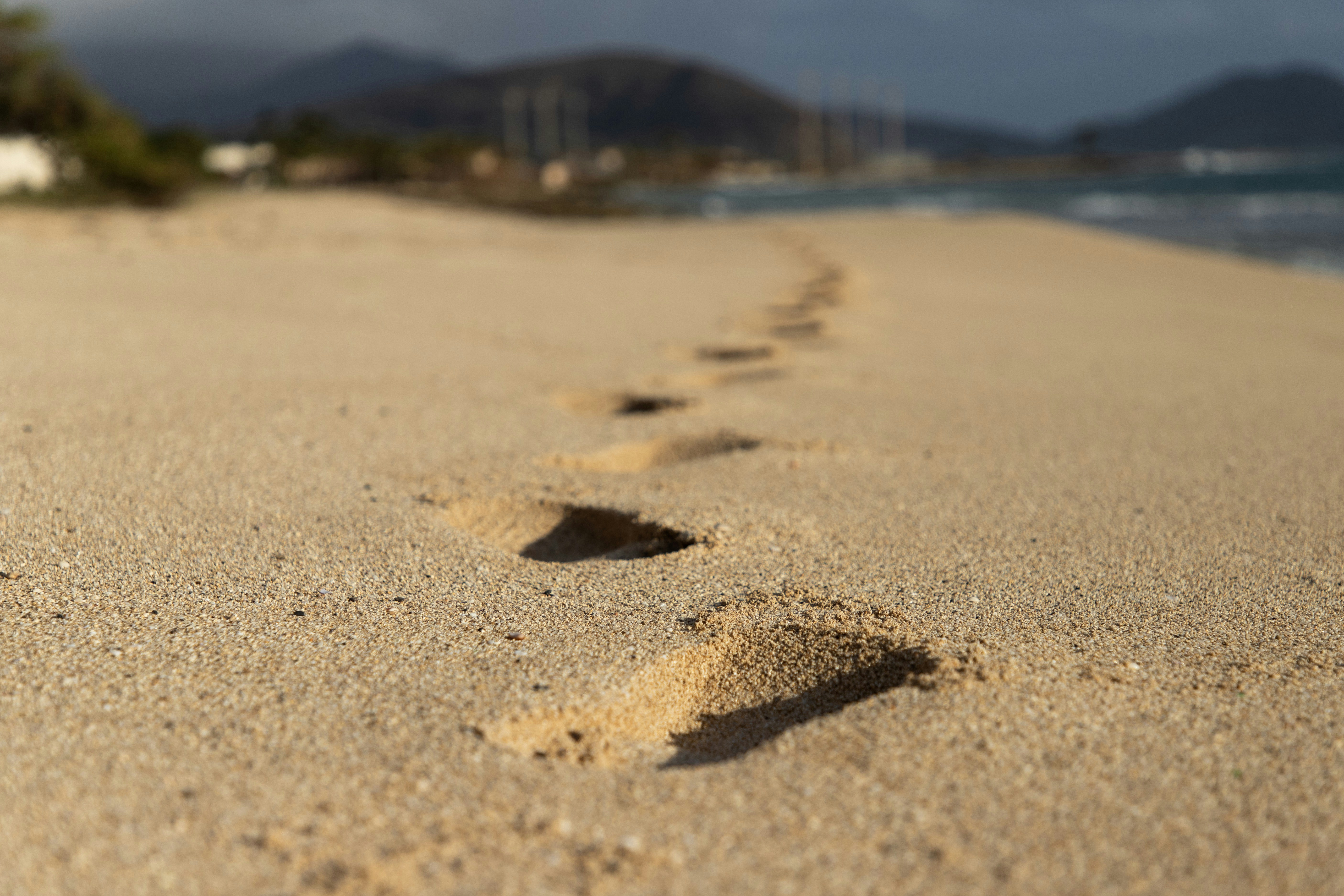 Footprint Trail Across Sunlit Sand Toward Distant Hills