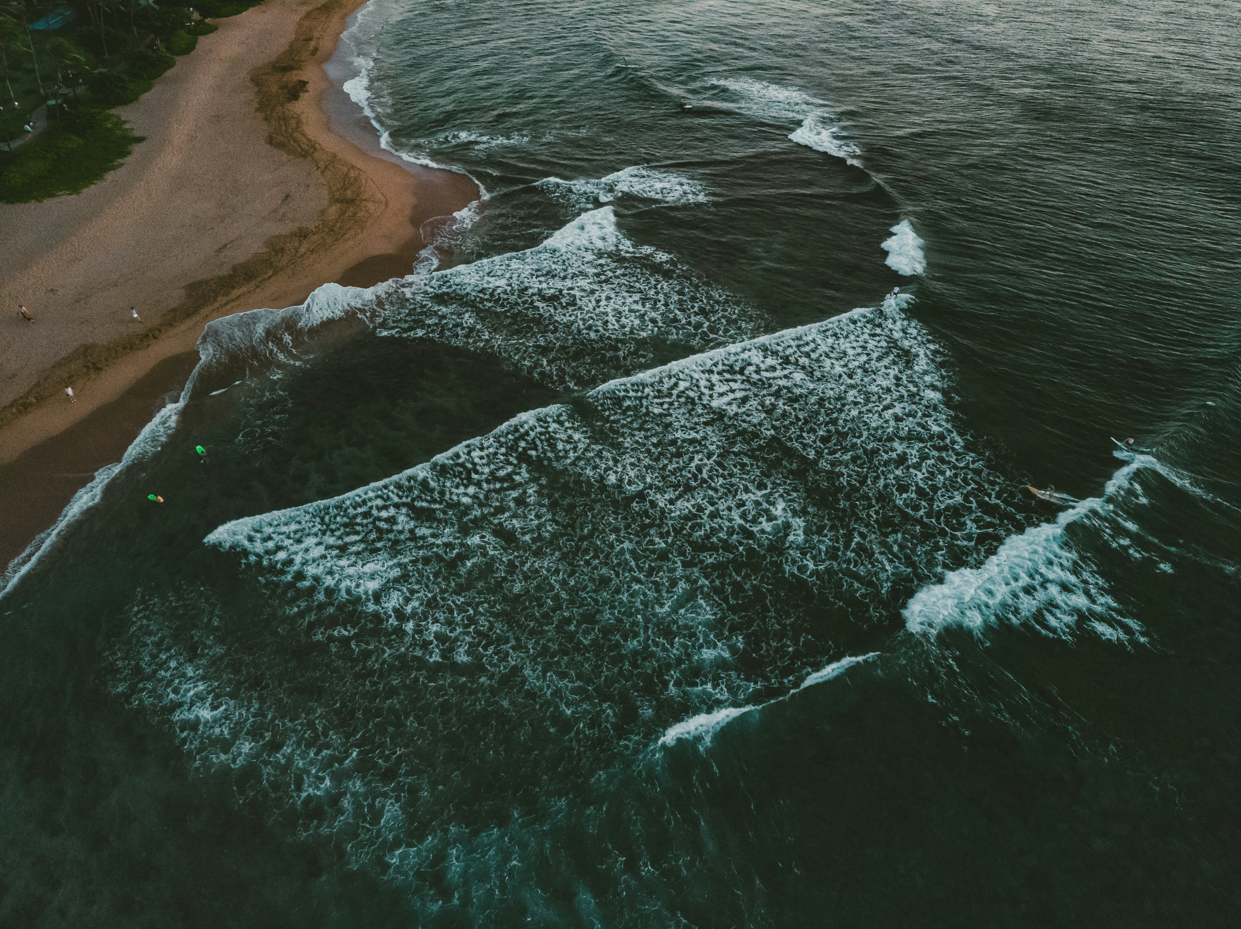 Waves crashing against a sandy beach with surfers navigating the surf.