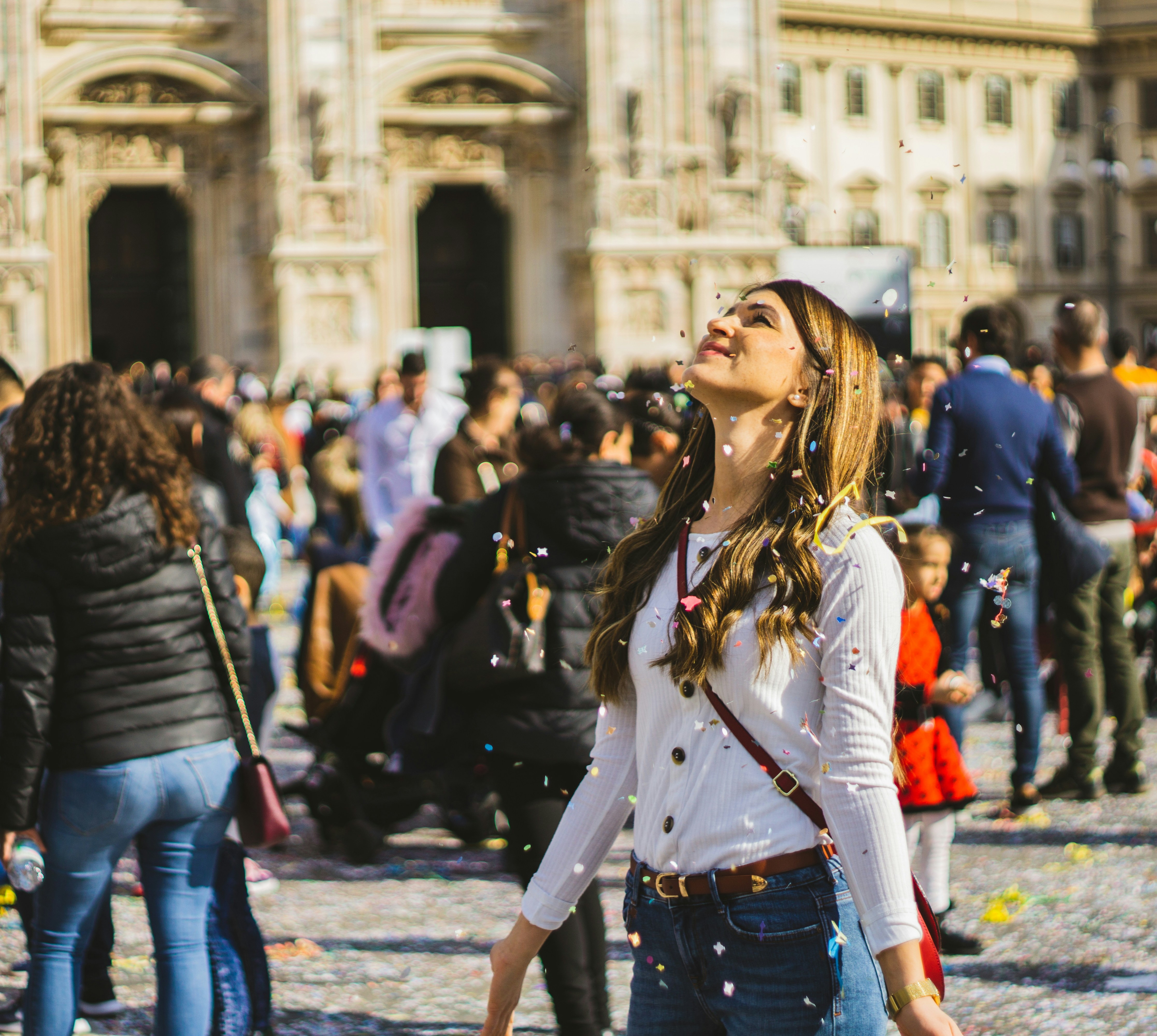 In the Sunlit Square: A Woman Surrounded by Confetti and Curious Gaze