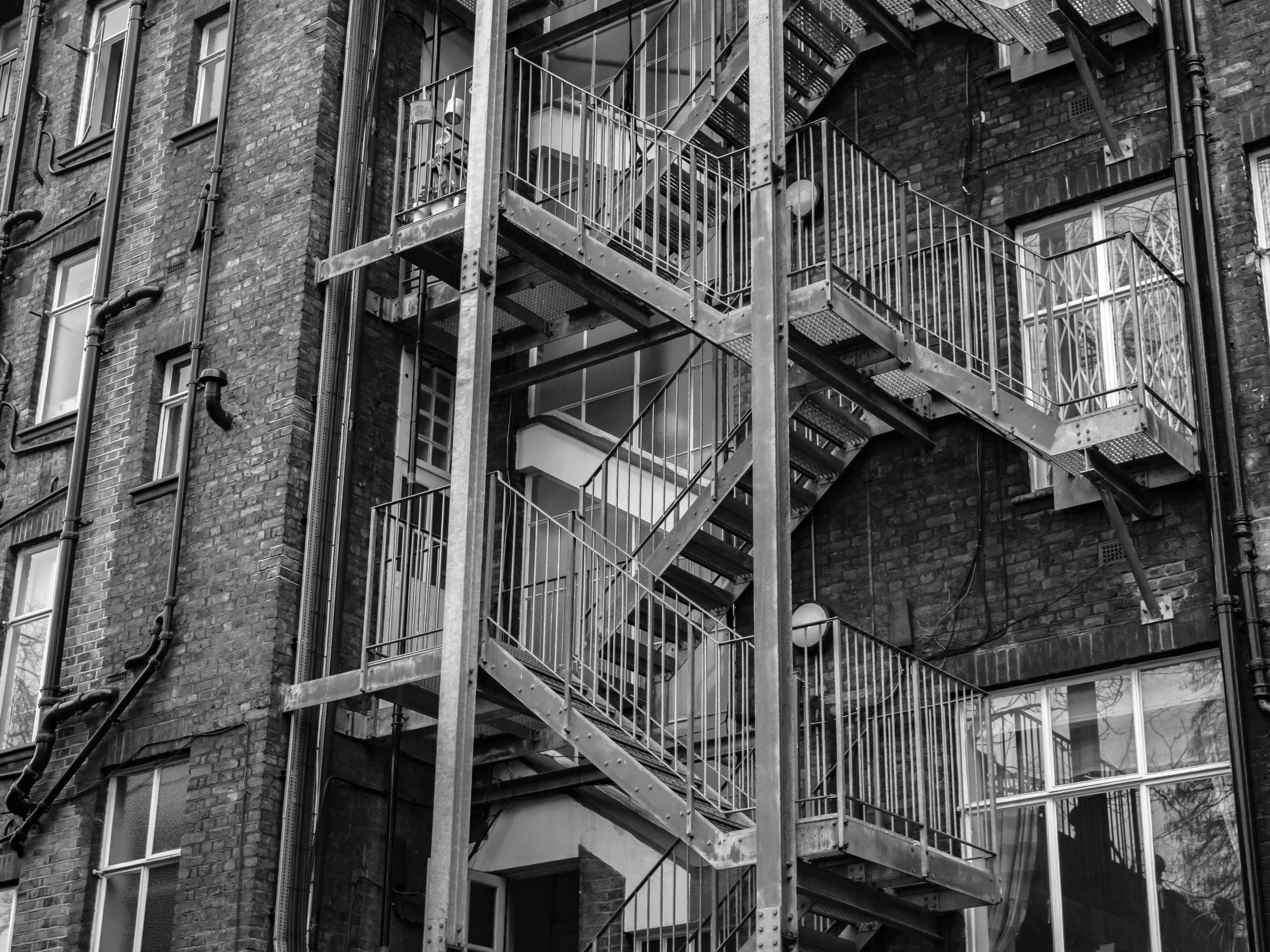Industrial-style fire escape staircase intertwined with a brick facade, showcasing architectural symmetry and urban life.