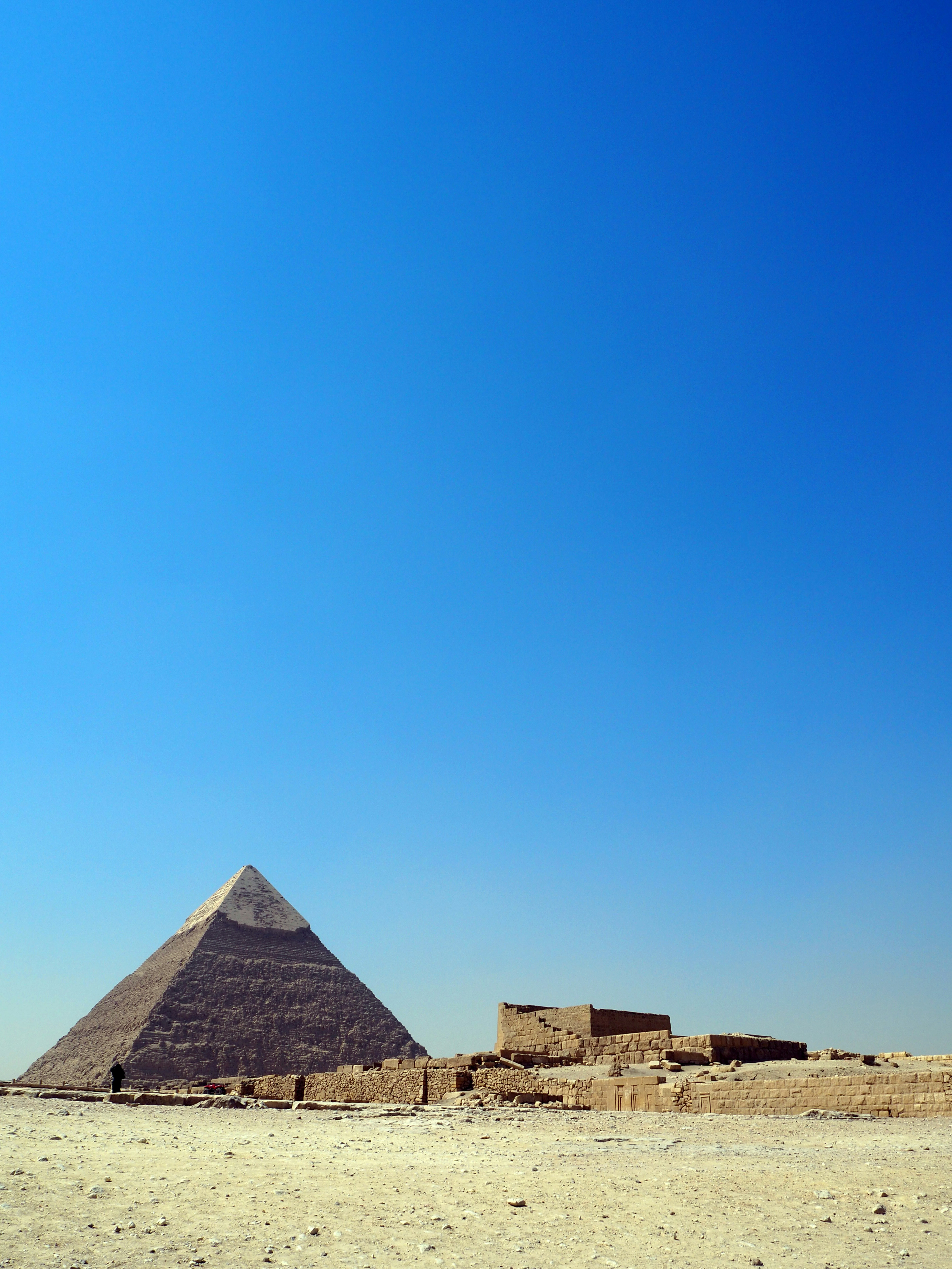 The Great Pyramid of Giza rises majestically against a clear blue sky, surrounded by ancient ruins and desert landscape.