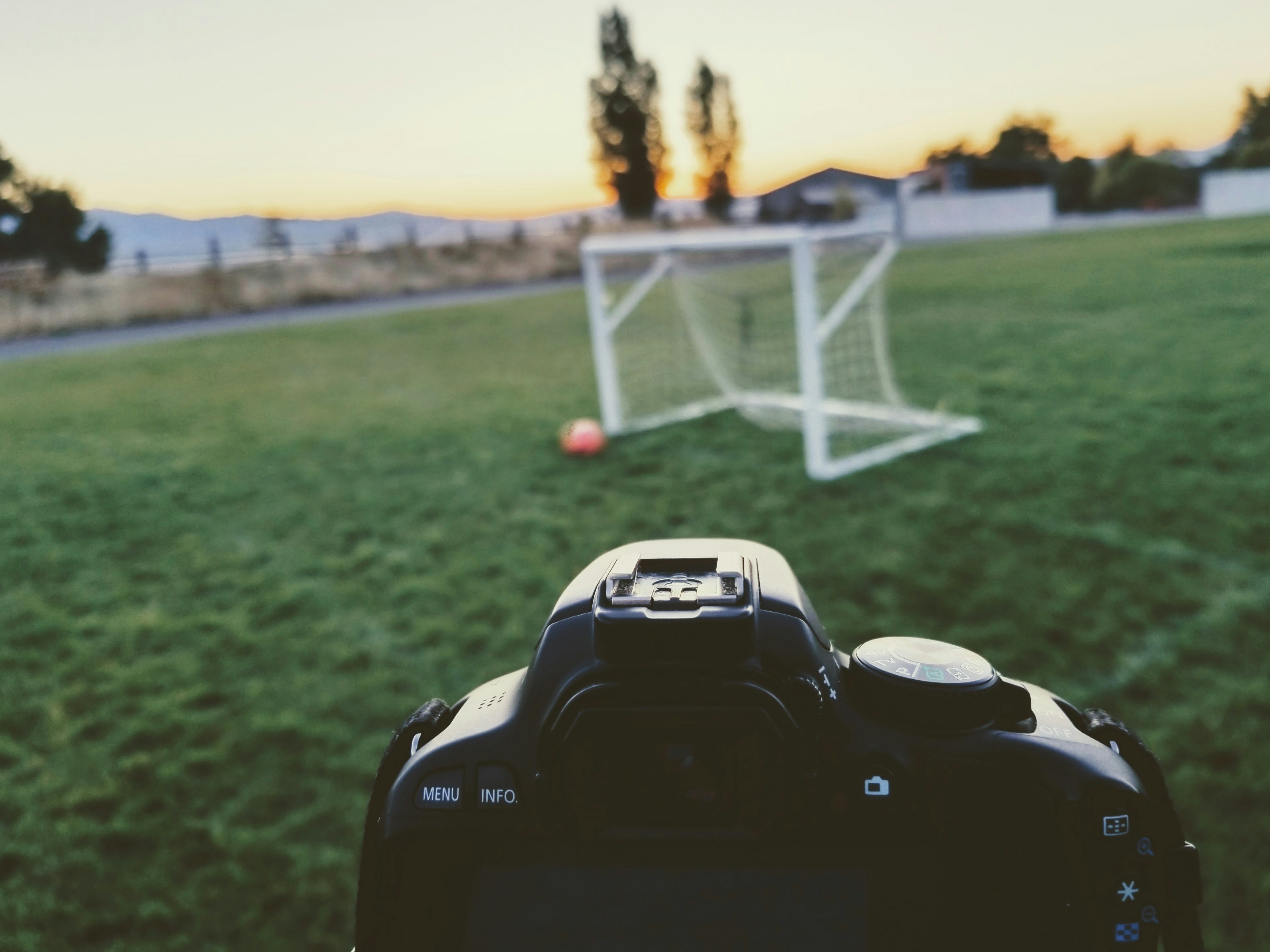 Ground-Level Focus at Dusk: A Camera Resting on Grass with a Distant Goal