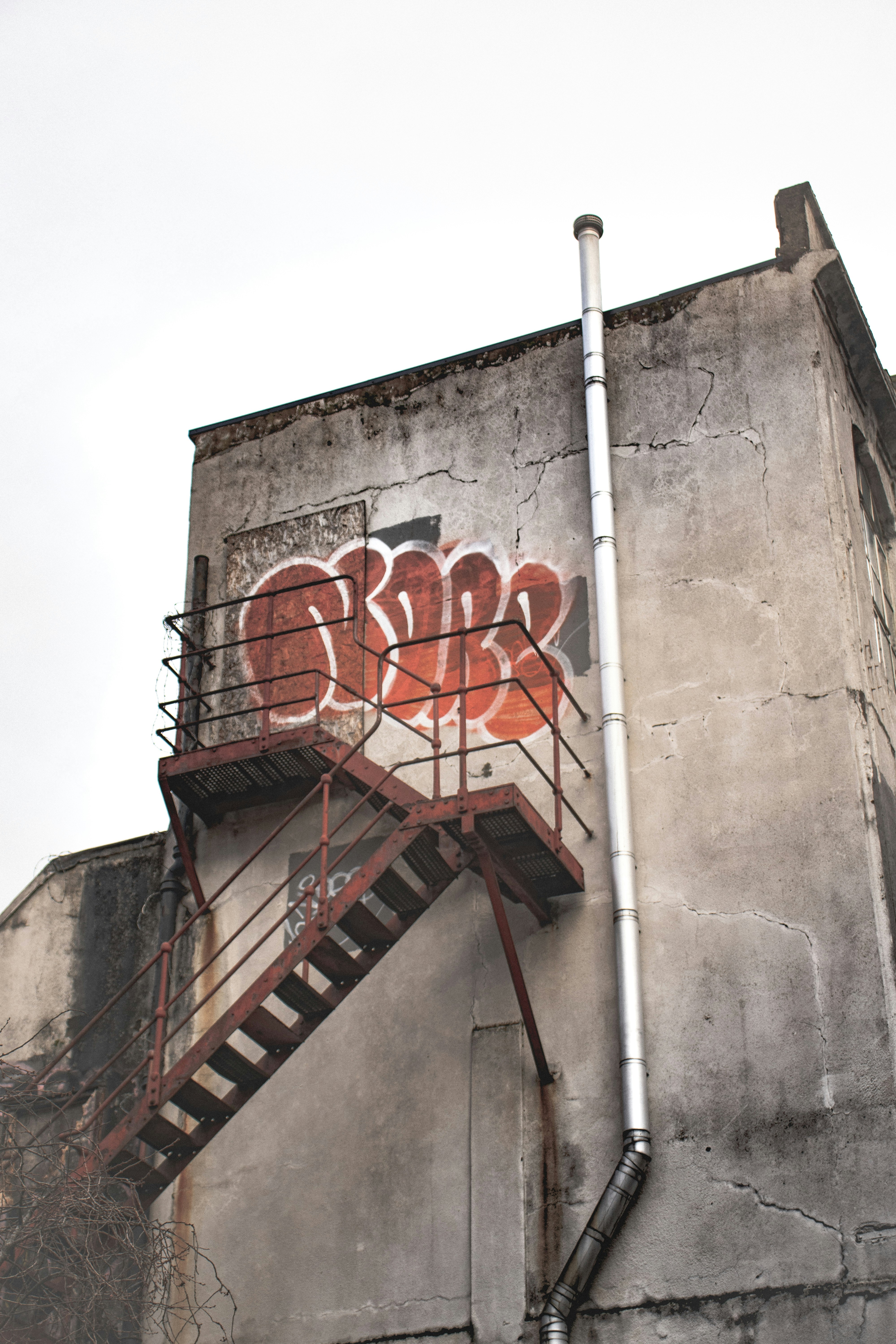 Cracked Facade Graffiti: A Rusted Staircase Framed by a Vertical Pipe