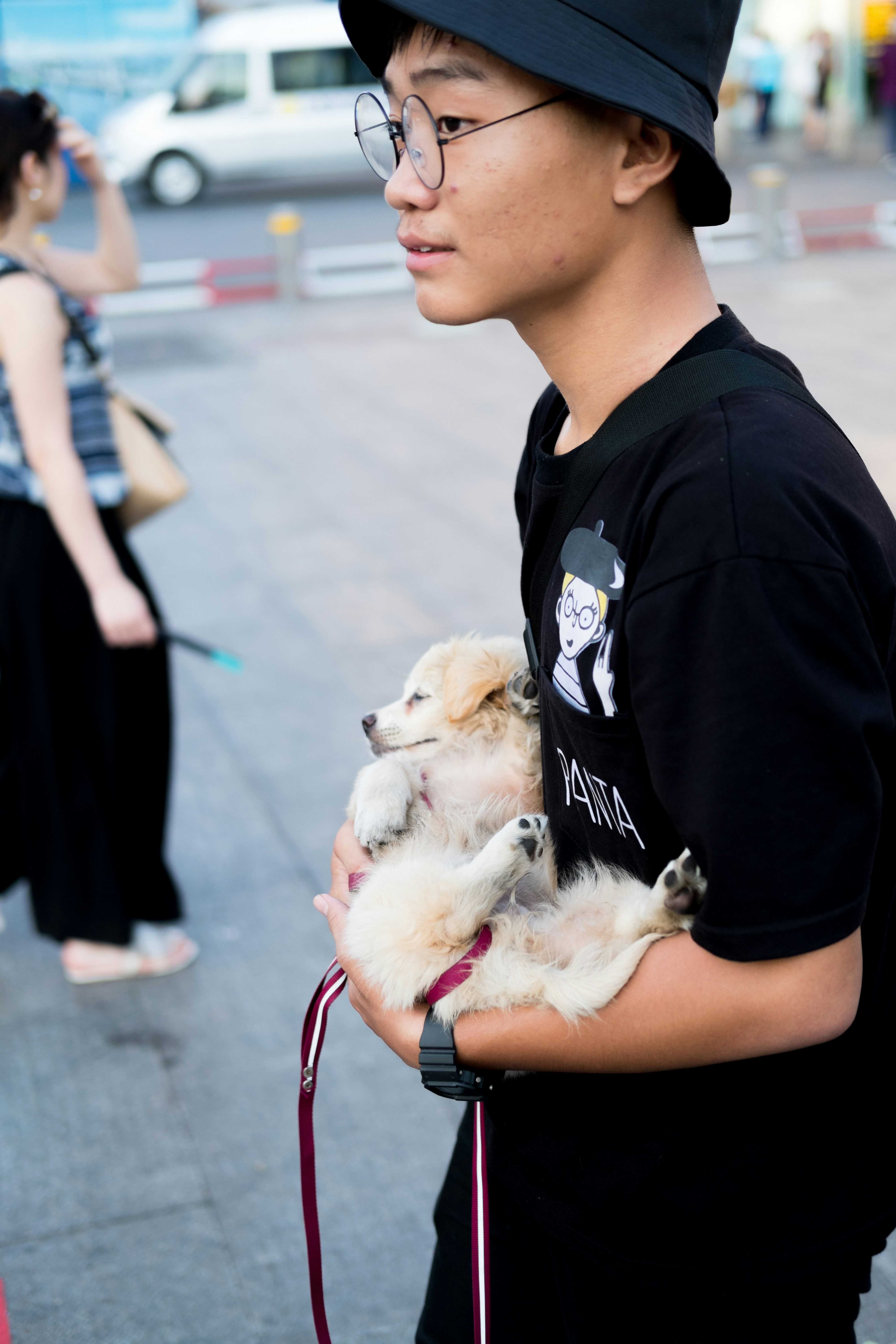 Young man holding a small, relaxed puppy in his arms while standing in a bustling urban environment.