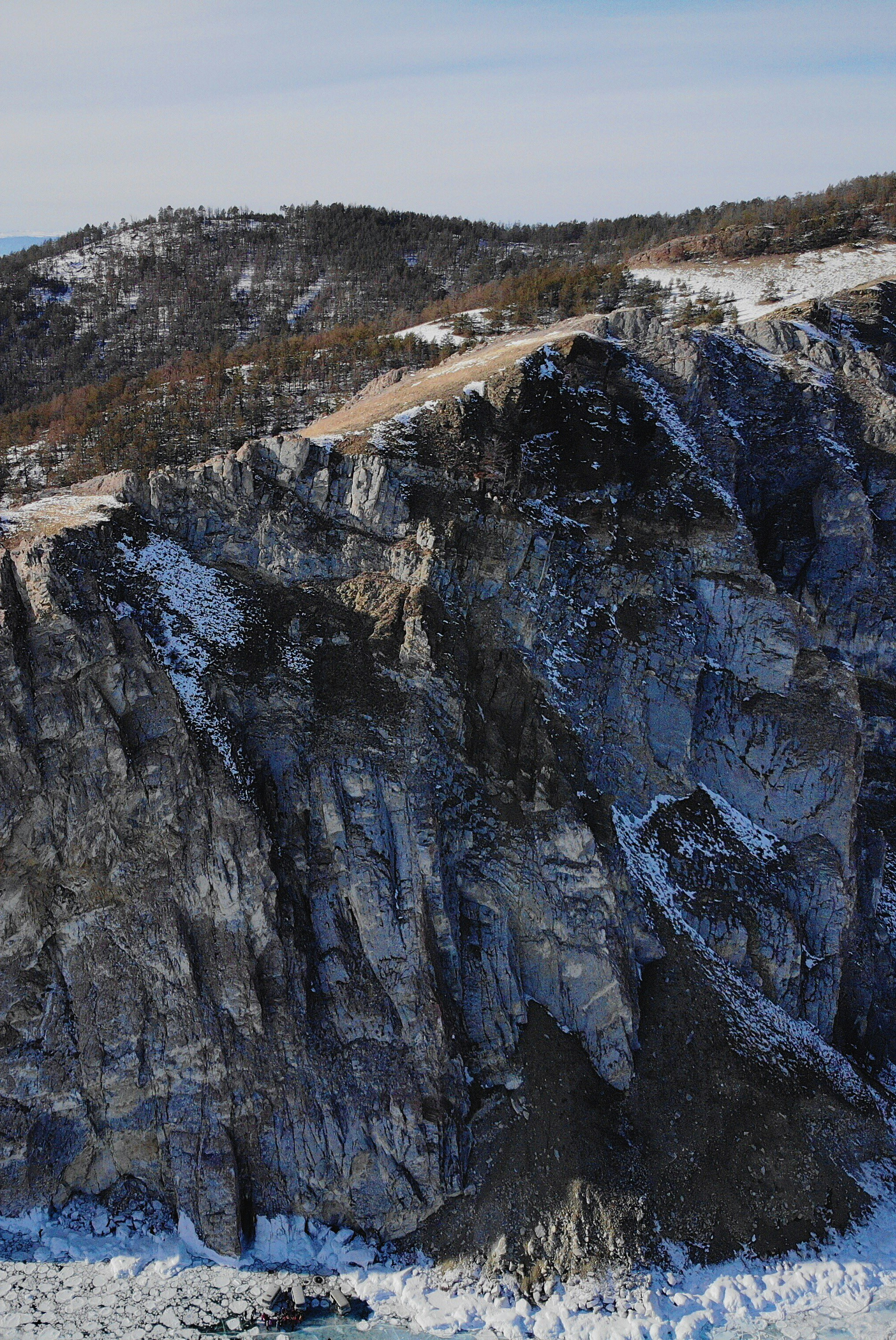 Majestic rocky cliffs adorned with patches of snow and rugged terrain, overlooking a frozen body of water. The scene captures the raw beauty of winter's embrace.