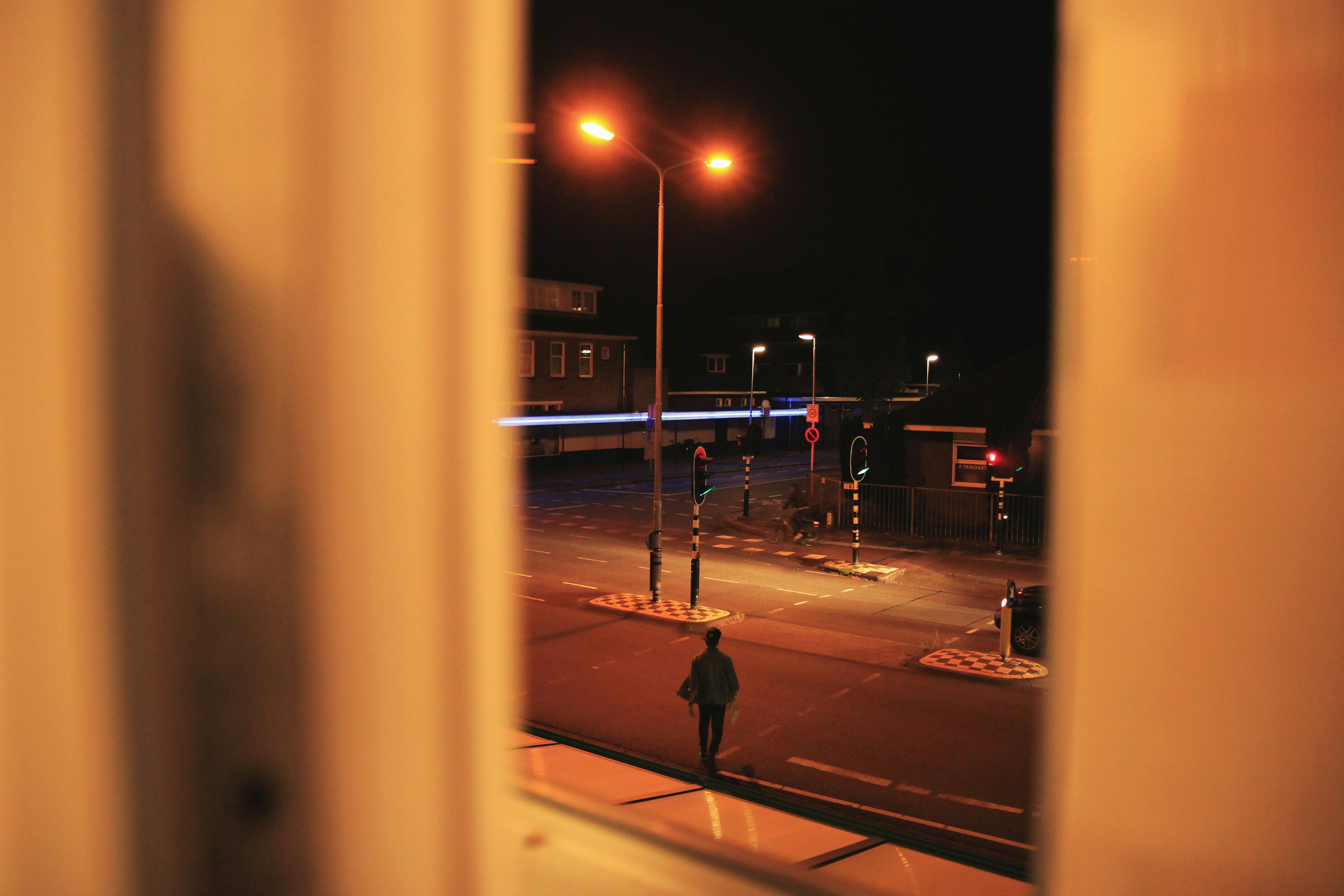 Silhouetted figure on a dimly lit street viewed through a window frame at night.