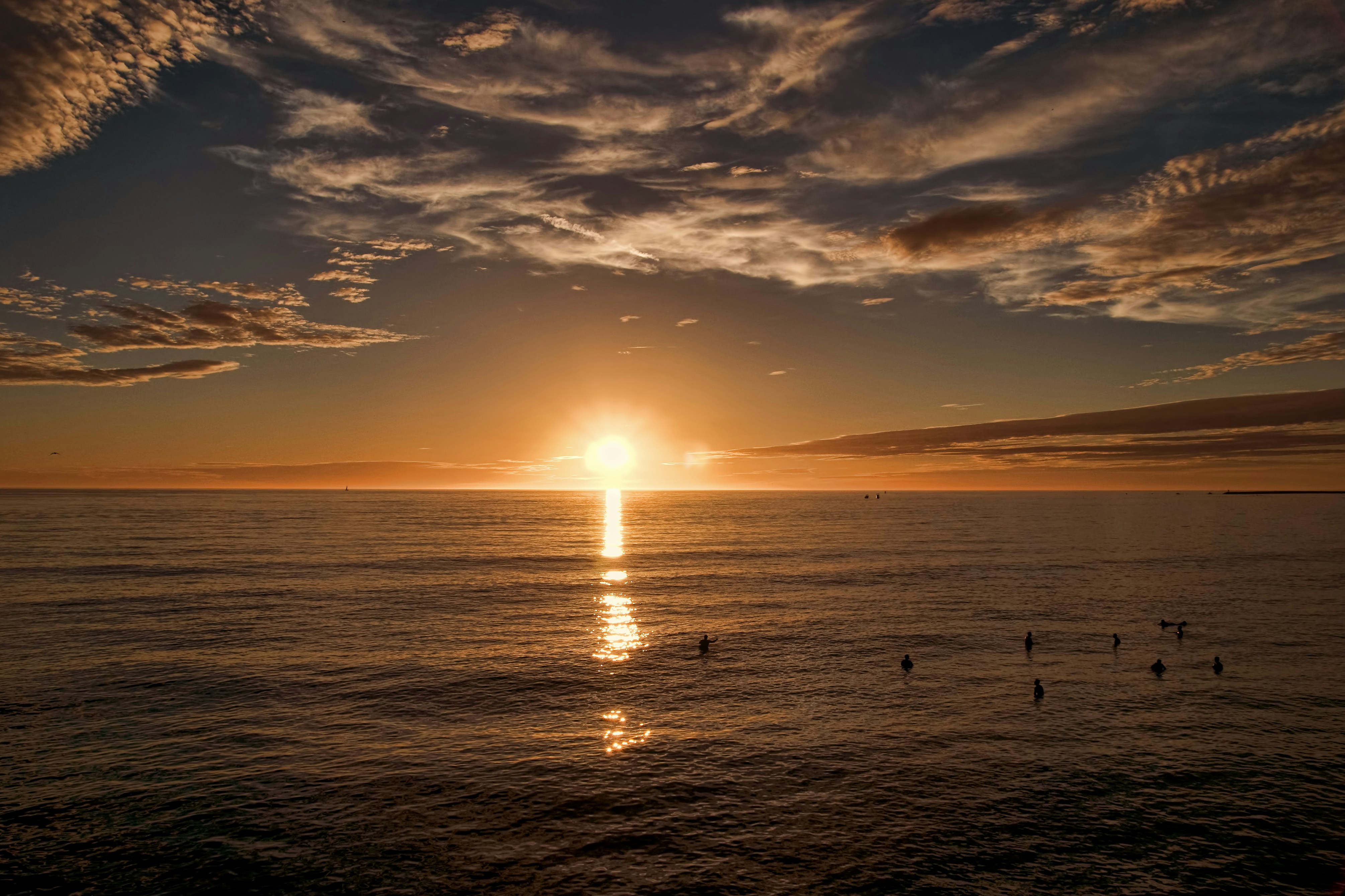 Sunset over a calm ocean with scattered clouds reflecting warm hues.
