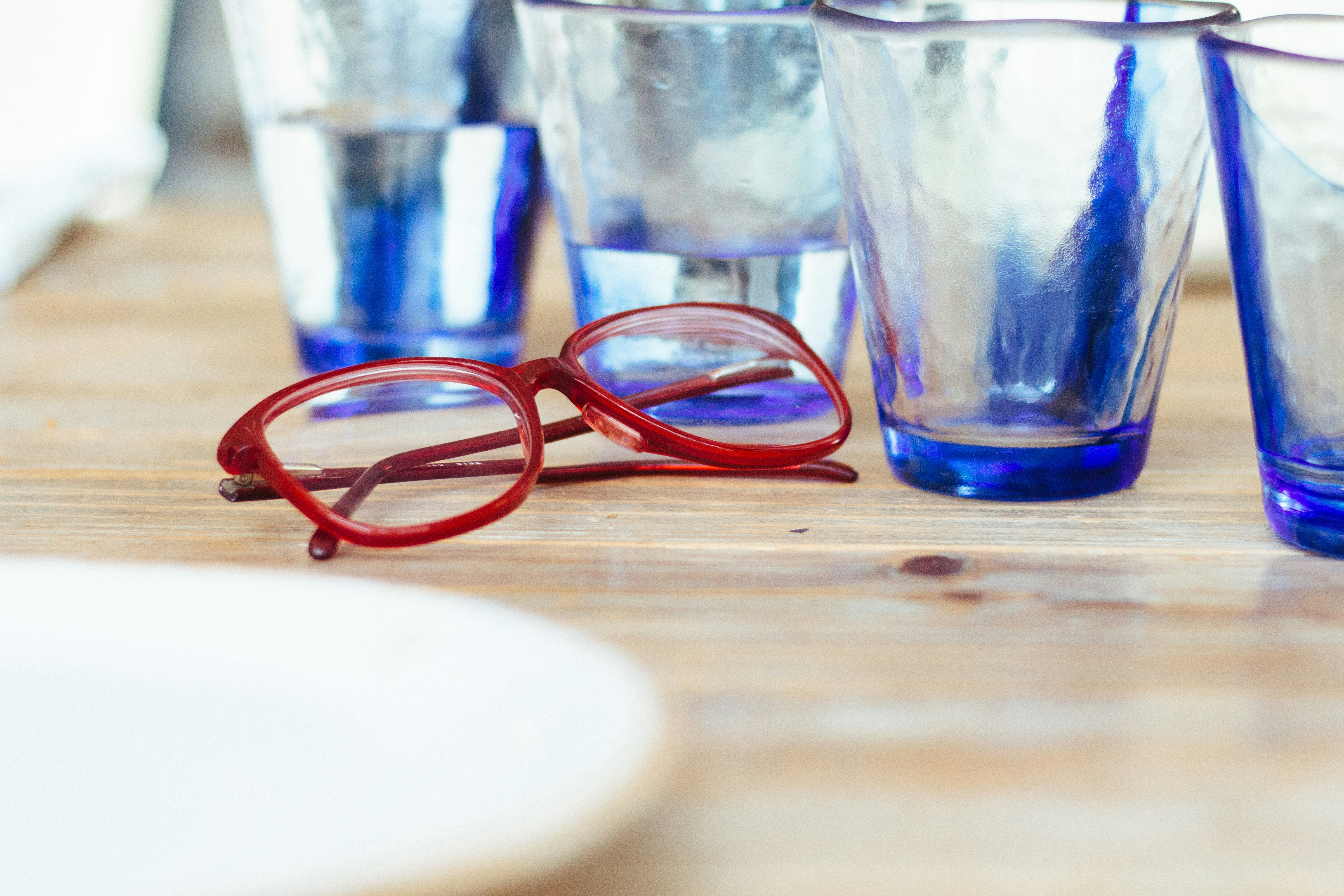 Crimson Eyewear Among cobalt Glasses on a Sunlit Wooden Table