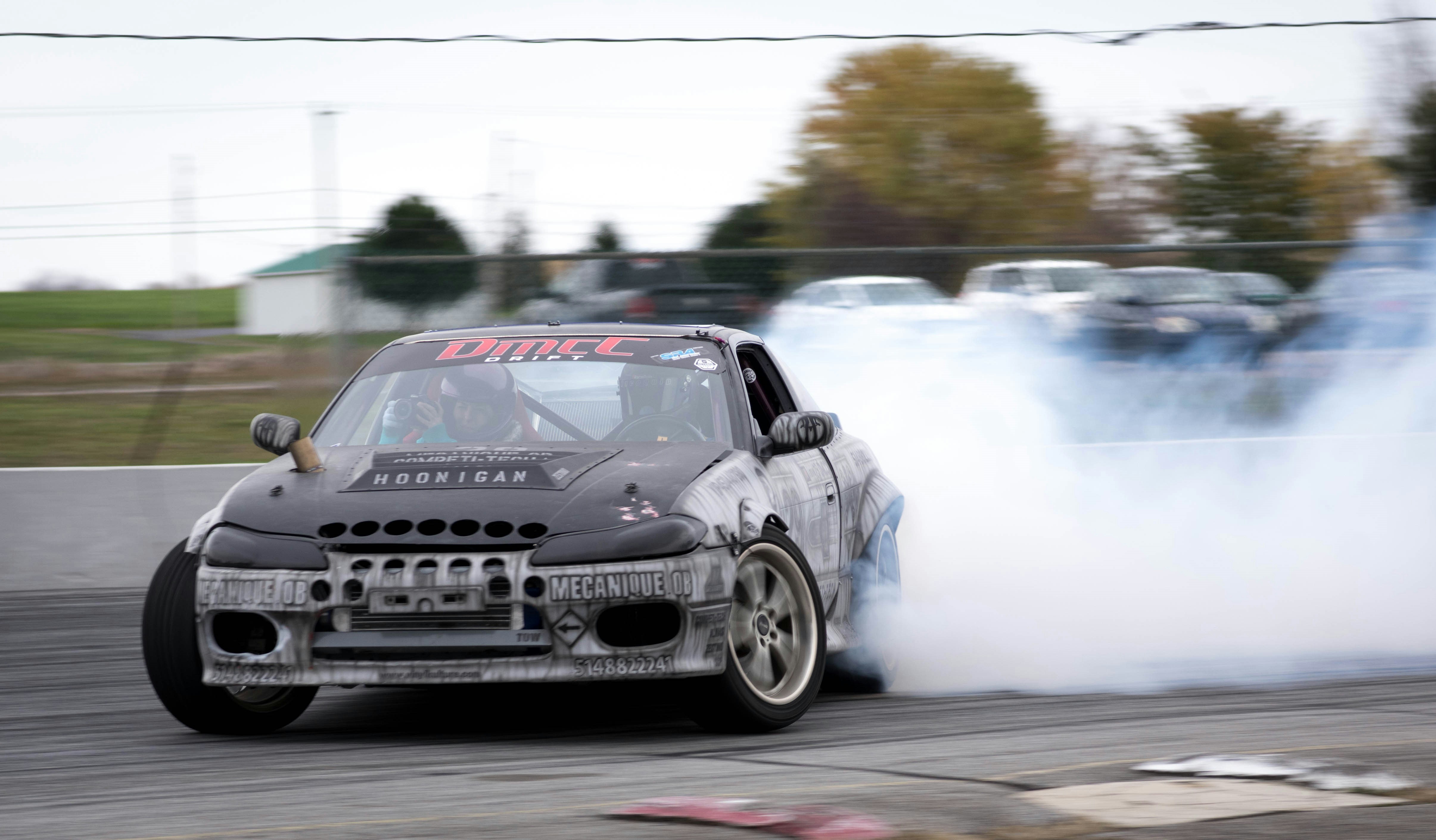 Car drifting on a track, surrounded by thick smoke with autumn trees in the background.