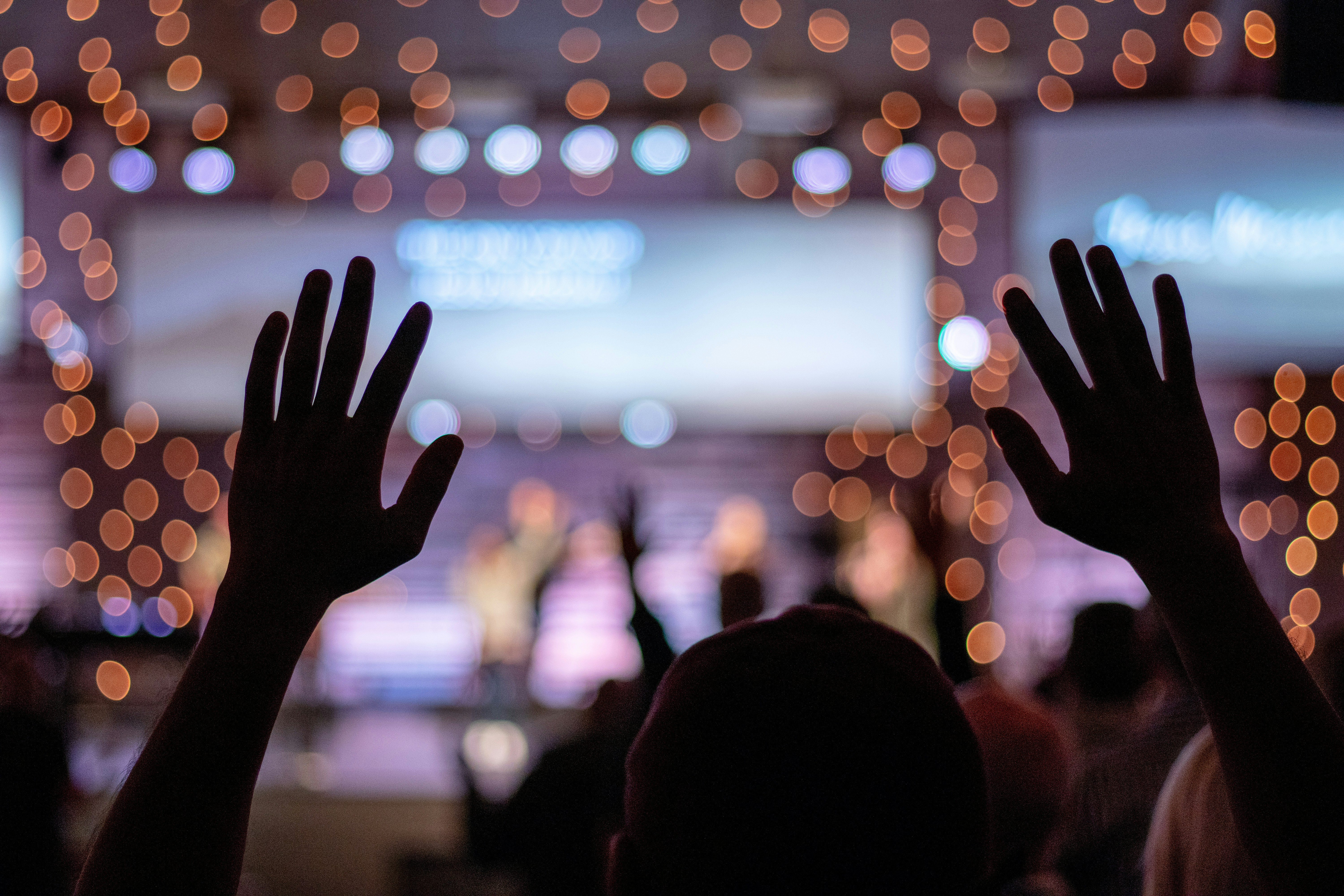 Hands raised in celebration amidst a blurred stage adorned with glowing lights, capturing a moment of collective joy.