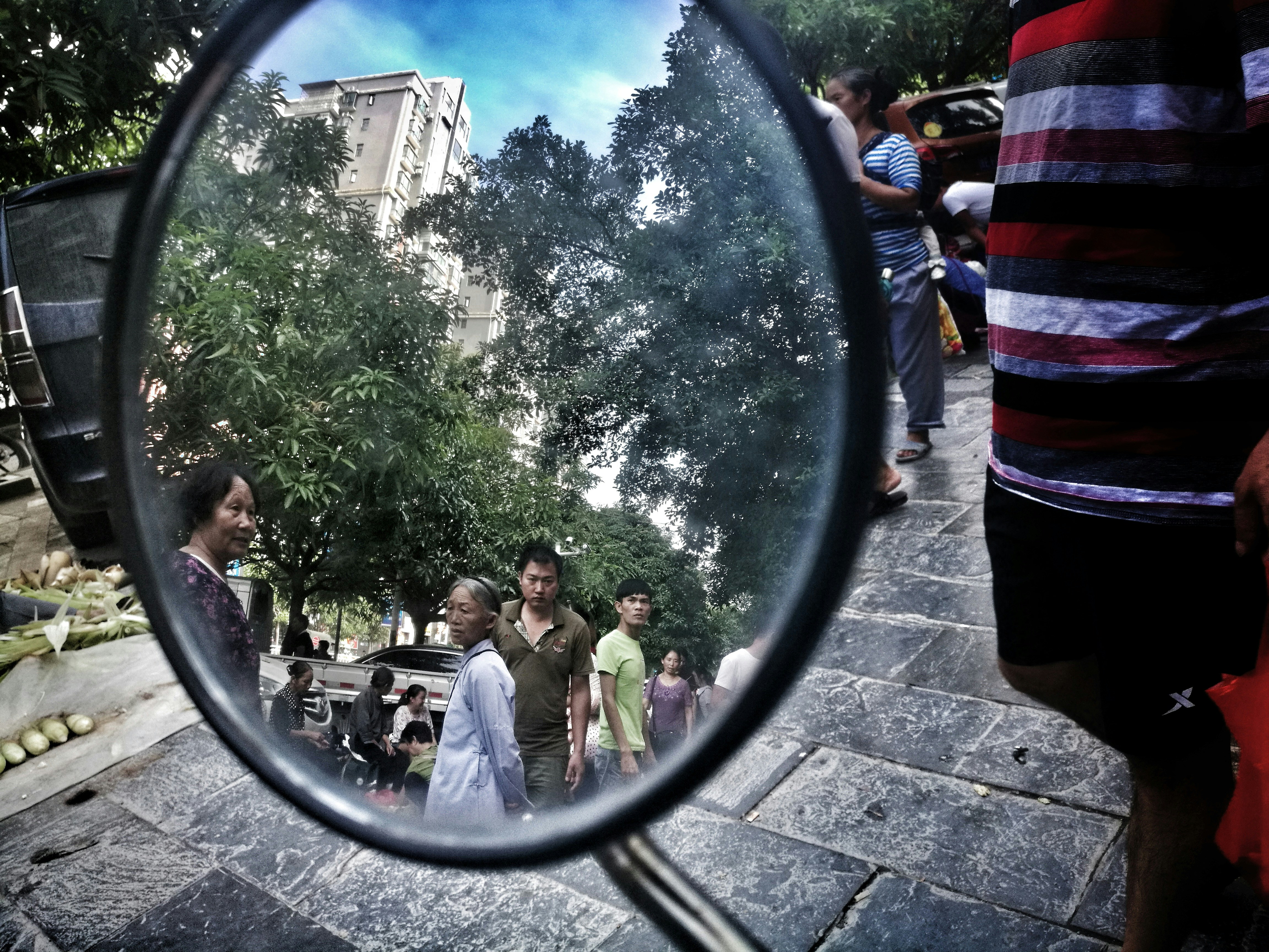 Photograph of a city staircase scene viewed through a handheld magnifier, focusing on a small group of pedestrians. The image contrasts close-up curiosity with the surrounding urban steps.