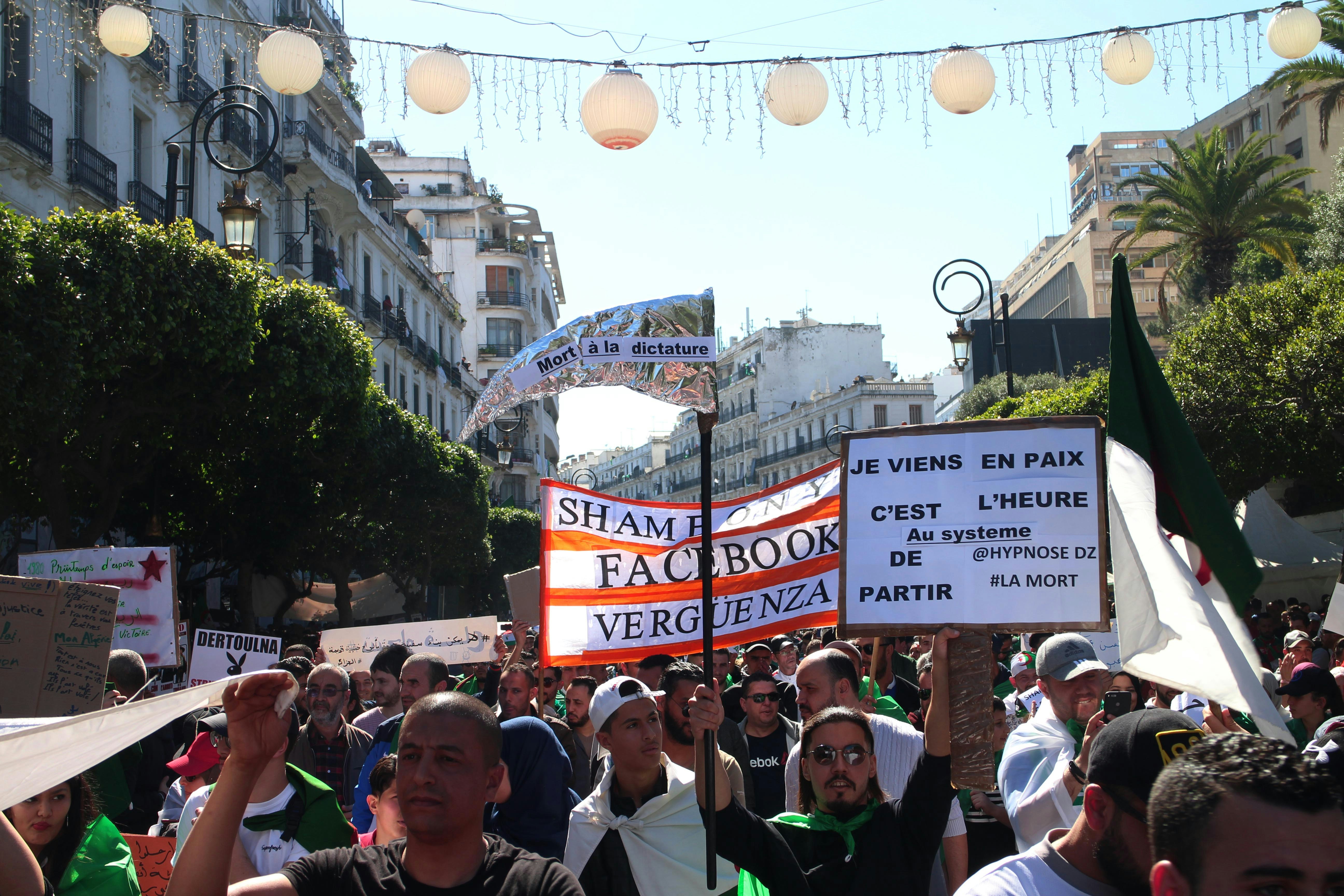 Crowd in a sunlit urban protest with banners and lanterns overhead