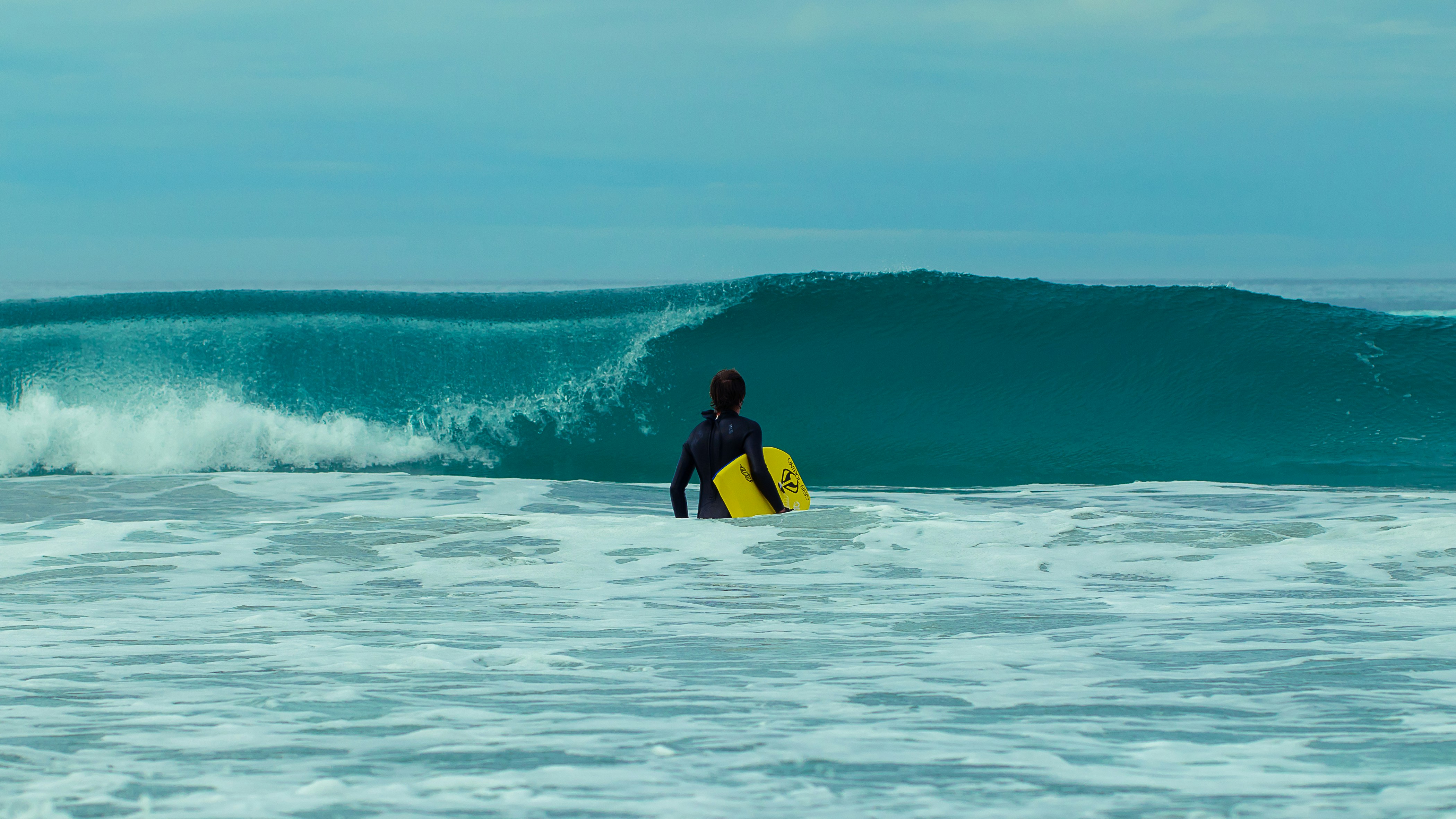 Personne portant un bodyboard en marchant dans l’eau vers la vague ...