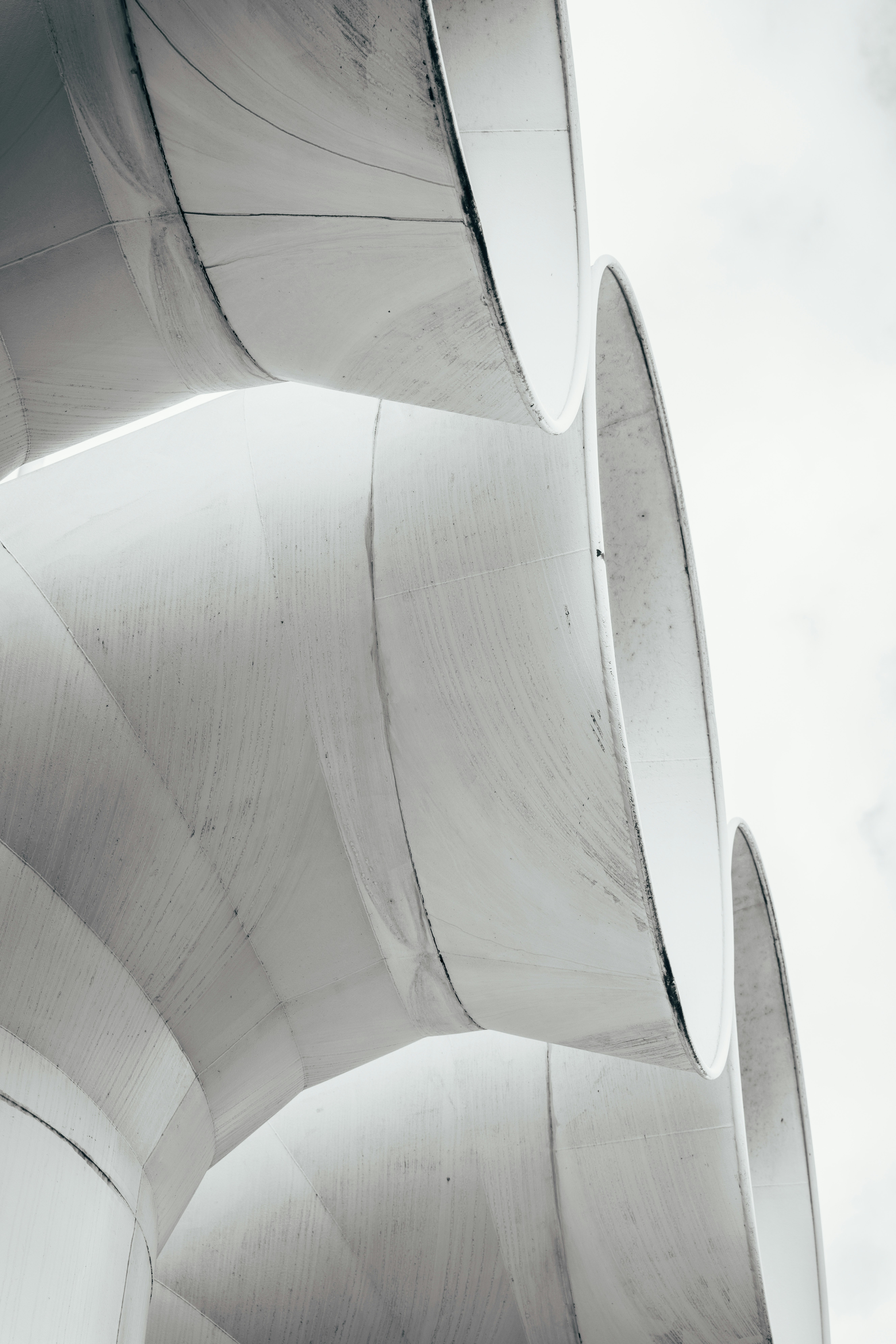 Abstract architectural forms of large concrete pipes against a cloudy sky. The interplay of light and shadow highlights the smooth surfaces.