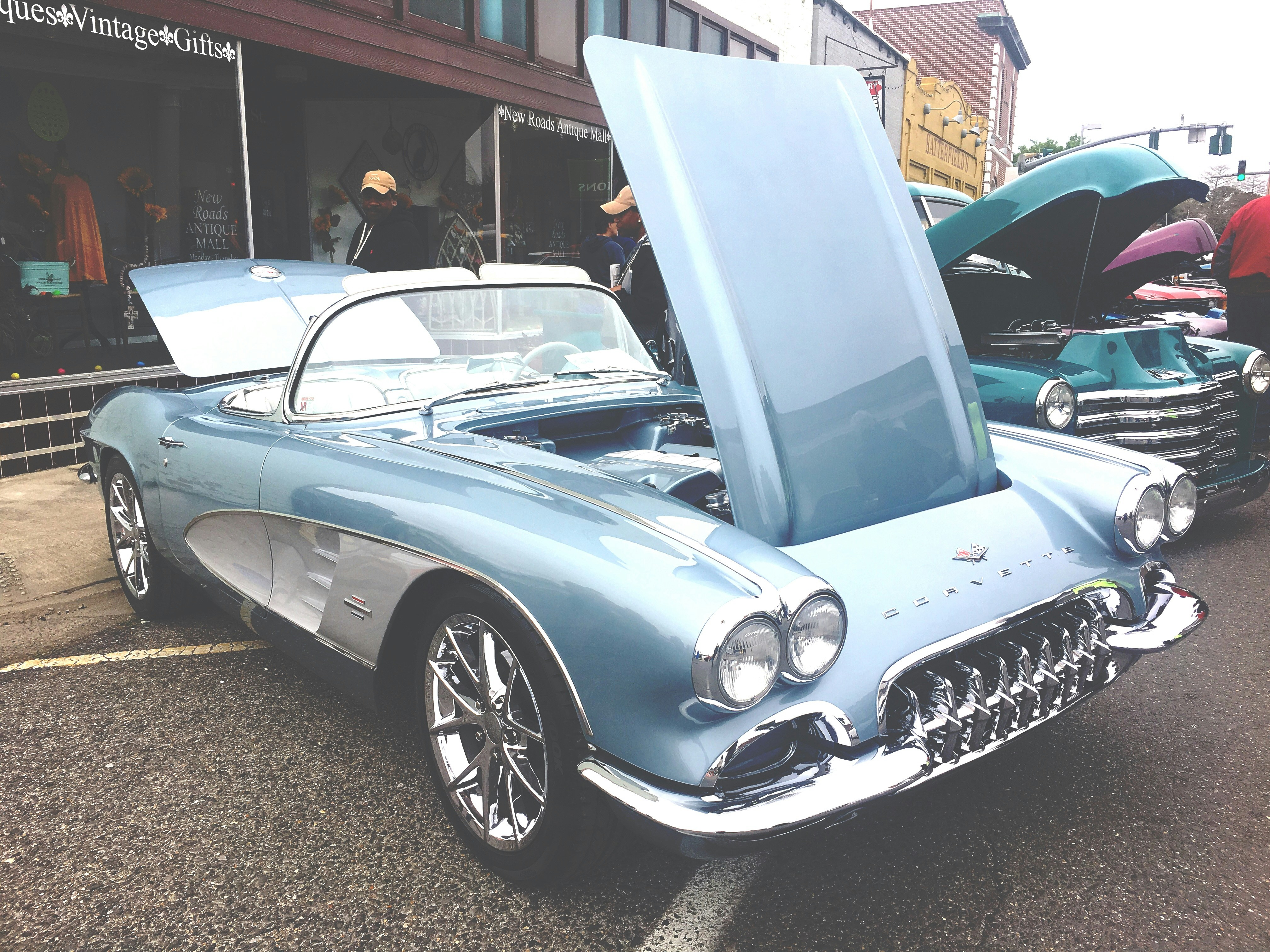 Classic blue convertible with raised hood showcased at a car event.